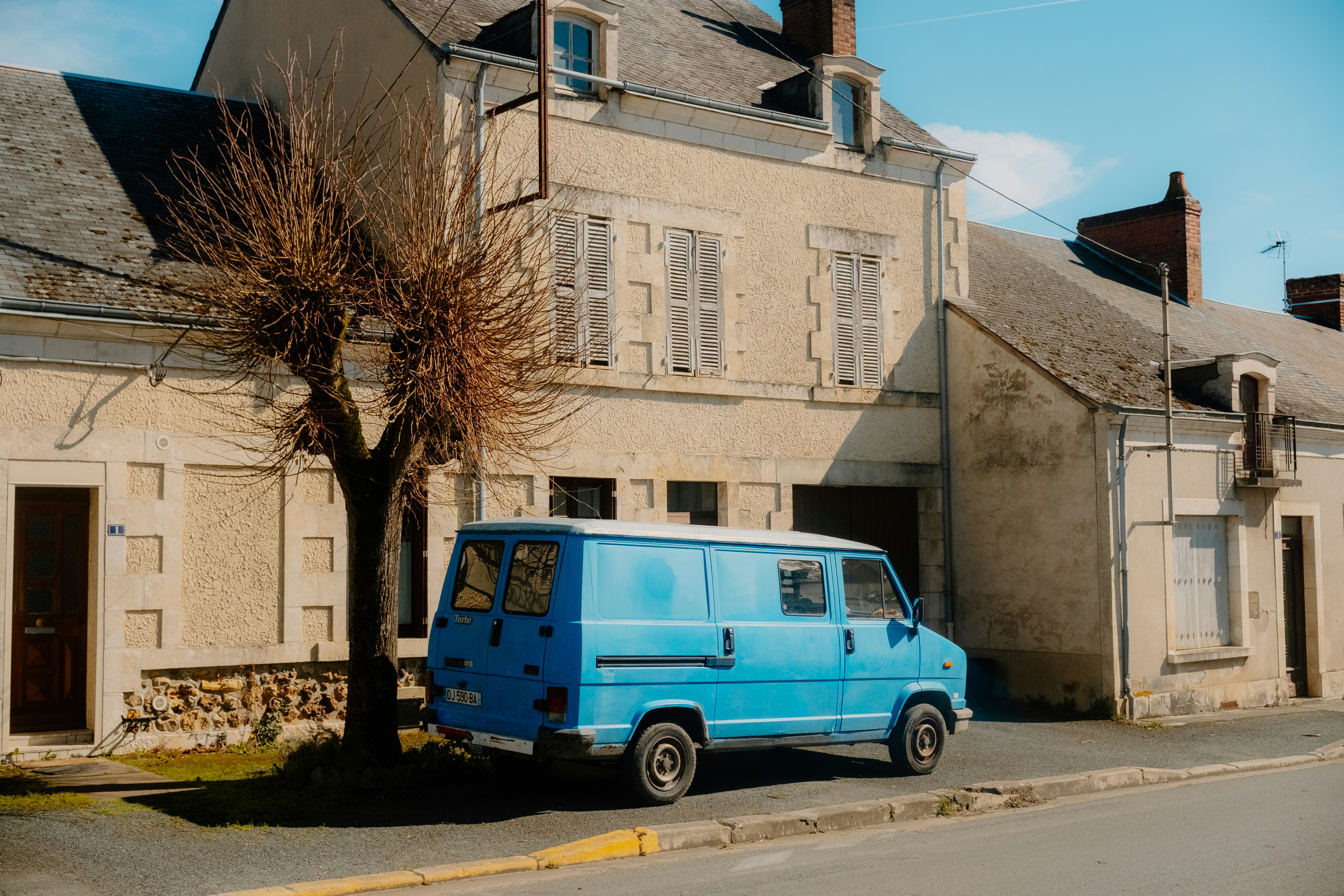 Azure Van on a Sunlit Street Between Stone Townhouses
