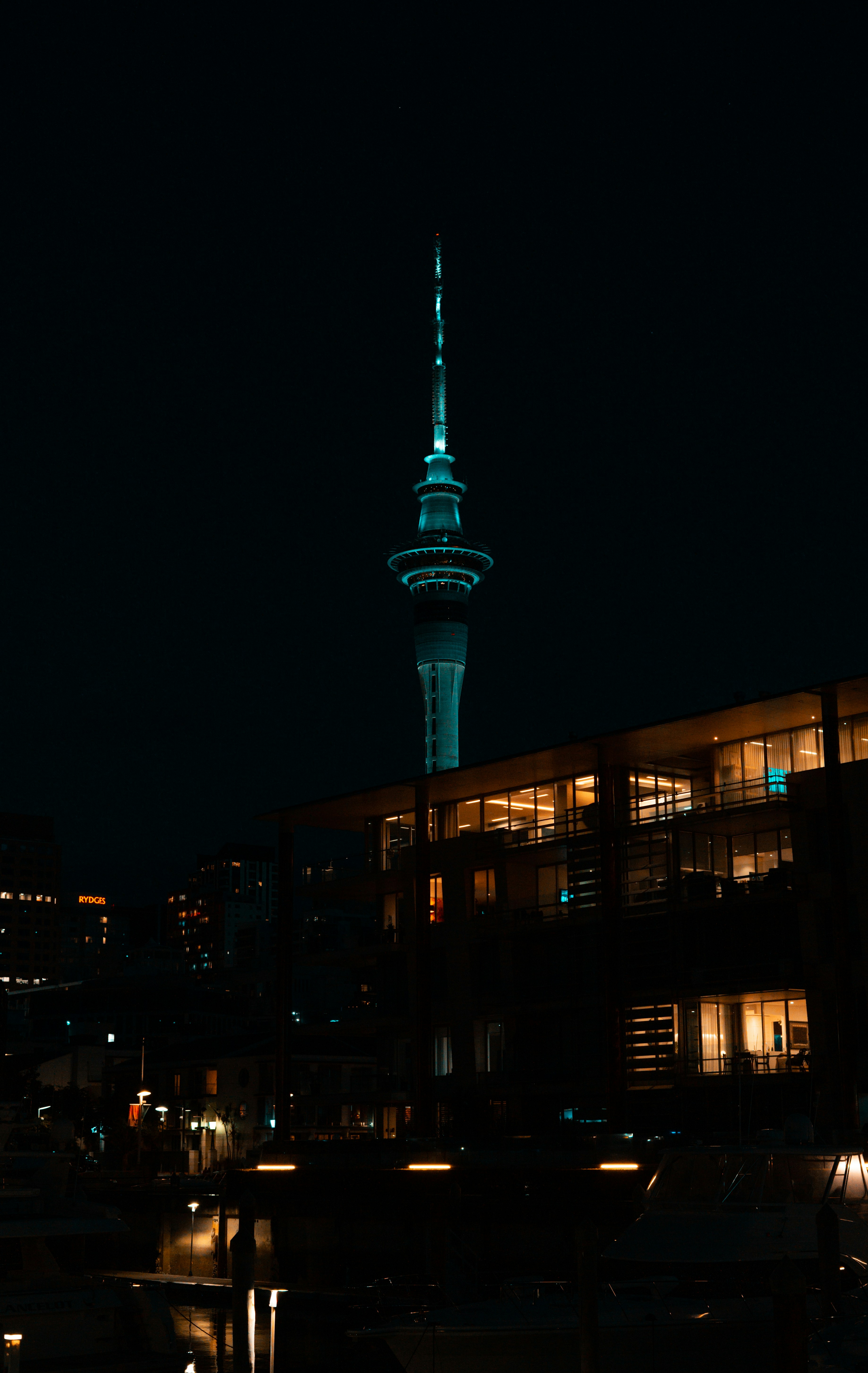 Teal Needle Rising Over a Quiet Marina at Night