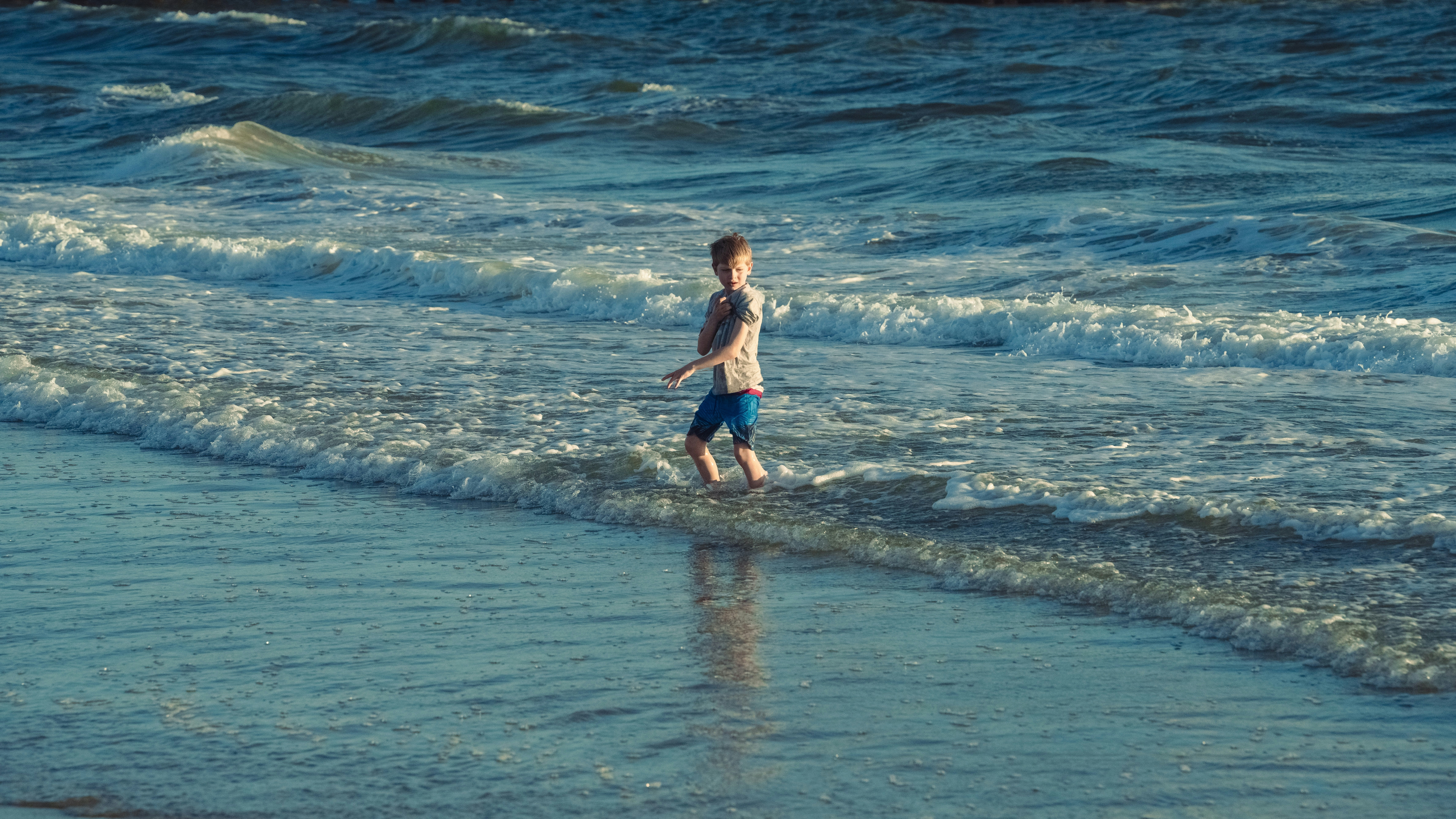 A young boy plays joyfully at the edge of the ocean, splashing in the waves on a warm summer day in Santa Monica. The late afternoon light reflects off the water, capturing a carefree moment of childhood by the sea. His laughter seems almost audible through the frame—a perfect snapshot of seaside fun and freedom.