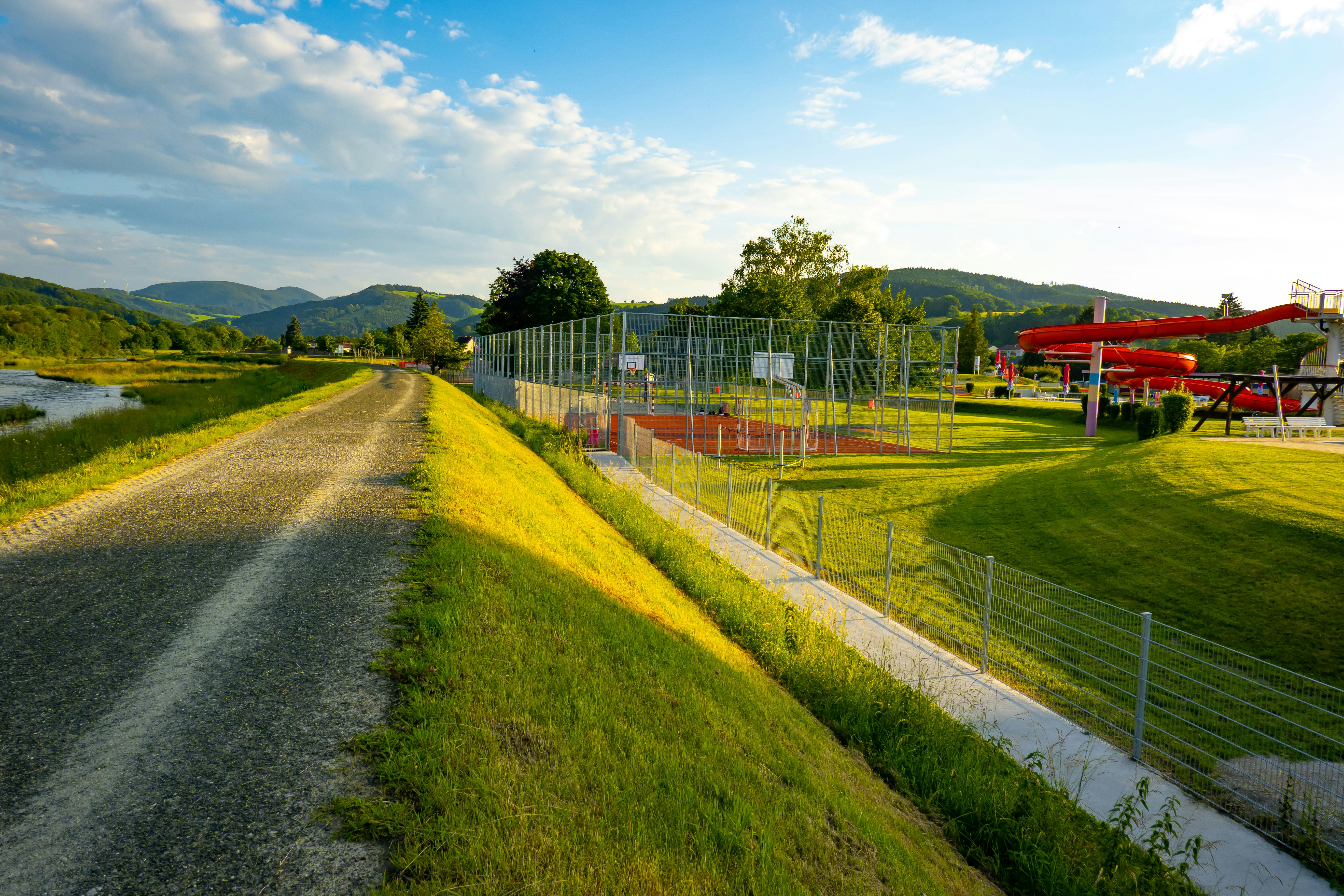 Gravel Ribbon by the River: A Sunlit Walk Toward Distant Hills
