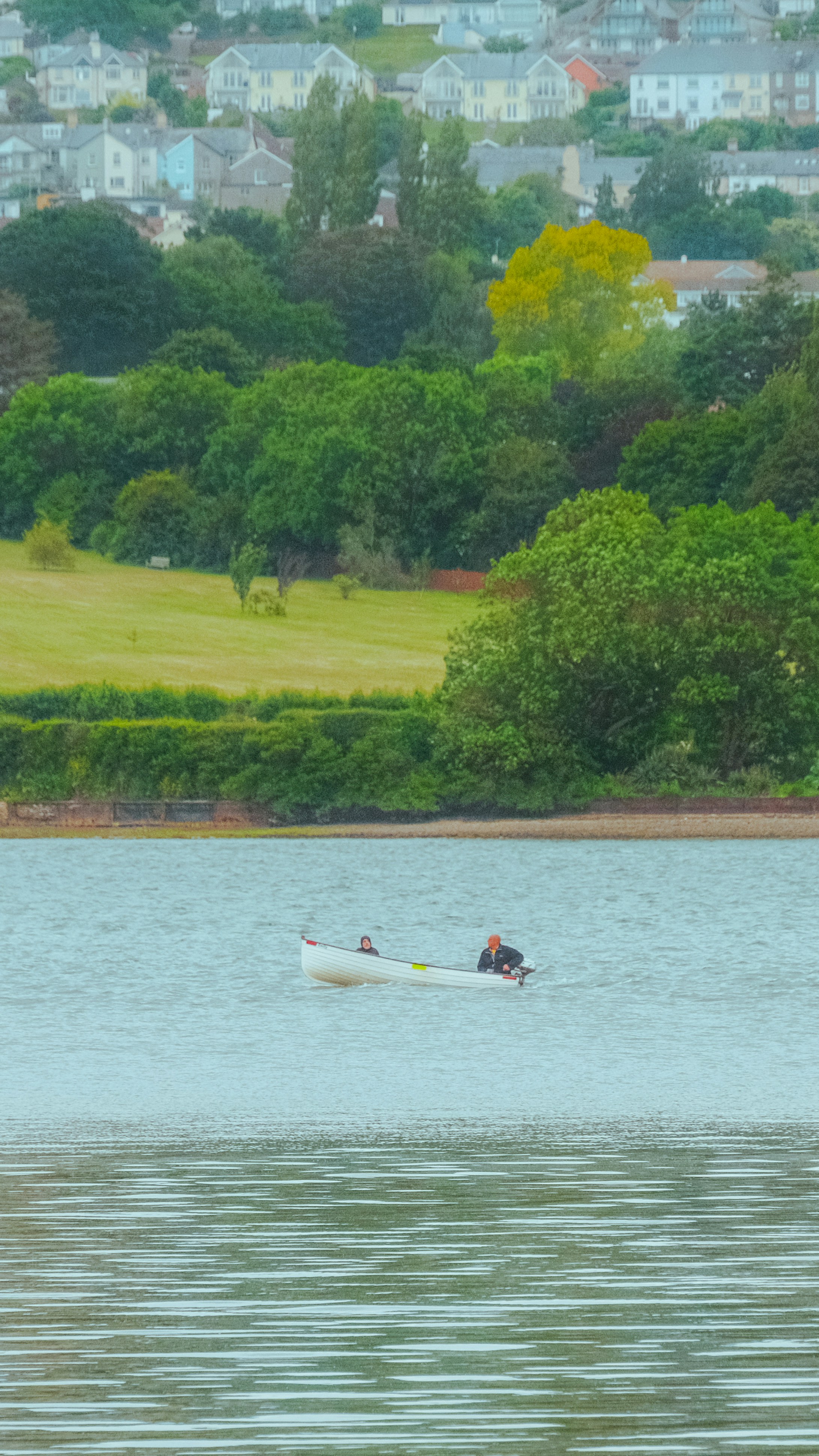 Boat on a calm river with riverside greenery and a distant village
