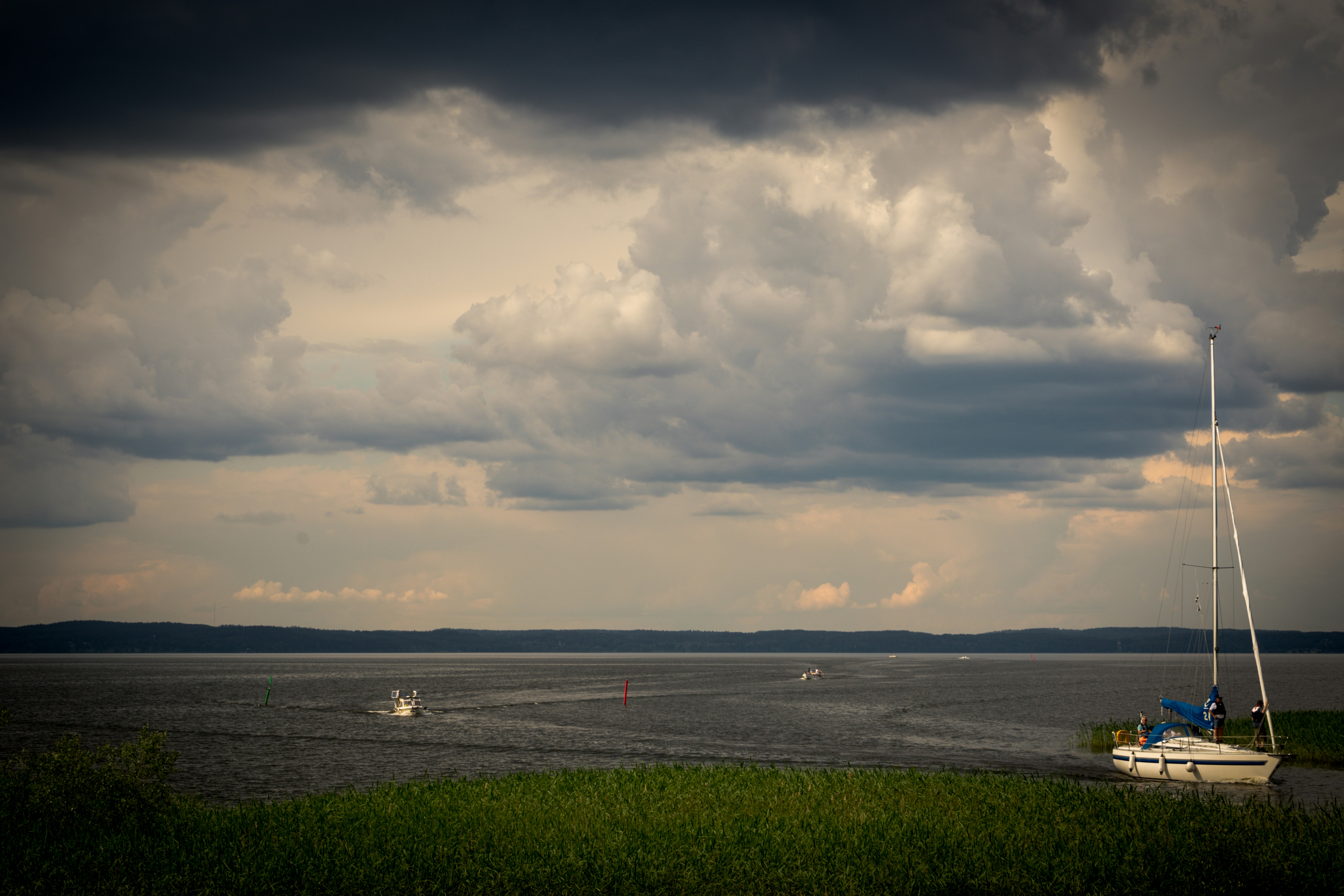 Sailboat anchored on calm water beneath dramatic, cloudy sky.