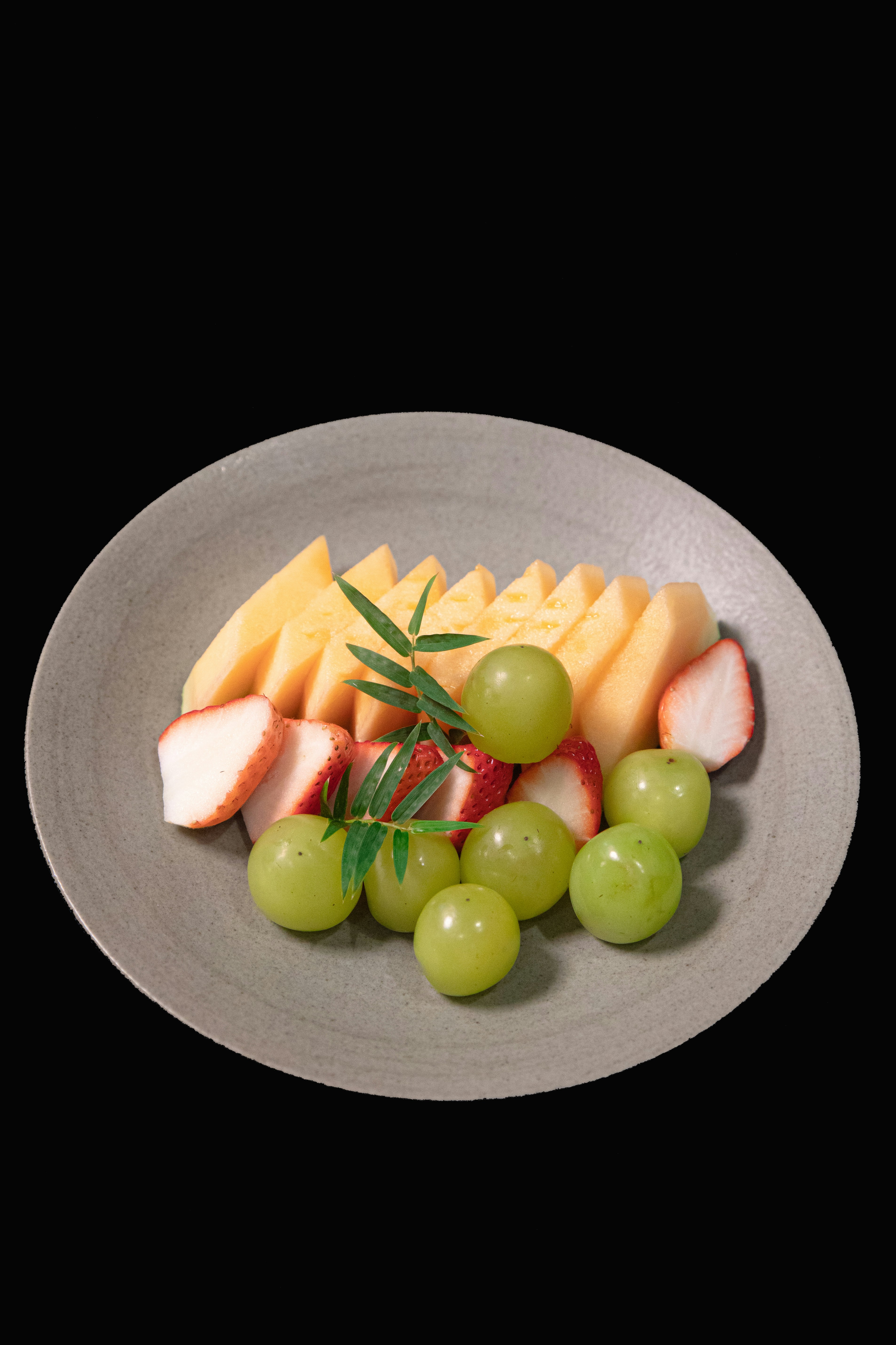 Grapes at Center Stage: A Quiet Palette of Melon and Strawberry on a Charcoal Plate