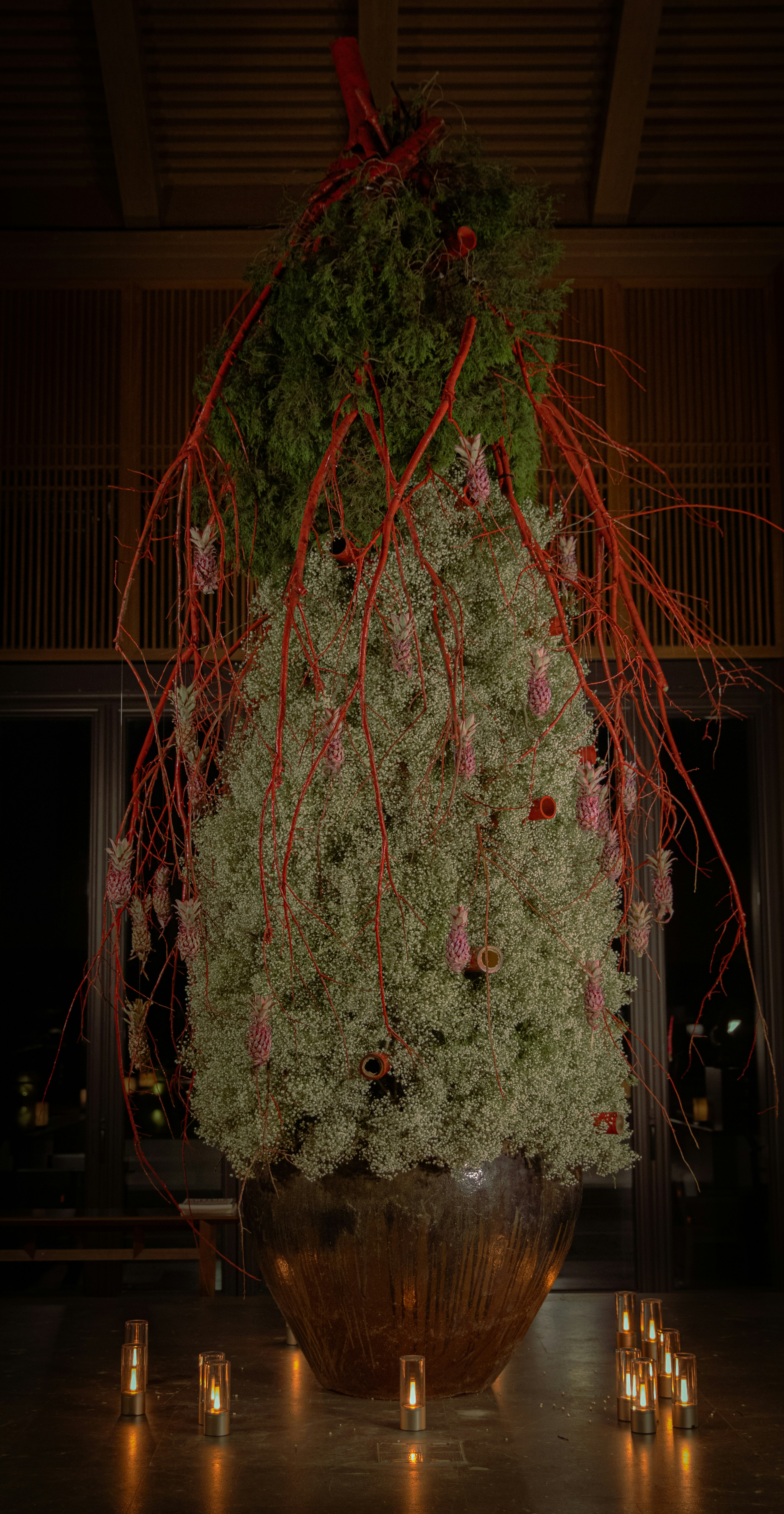 A striking floral arrangement featuring vibrant red branches and delicate white blooms, set against a dark backdrop with softly glowing candles below.
