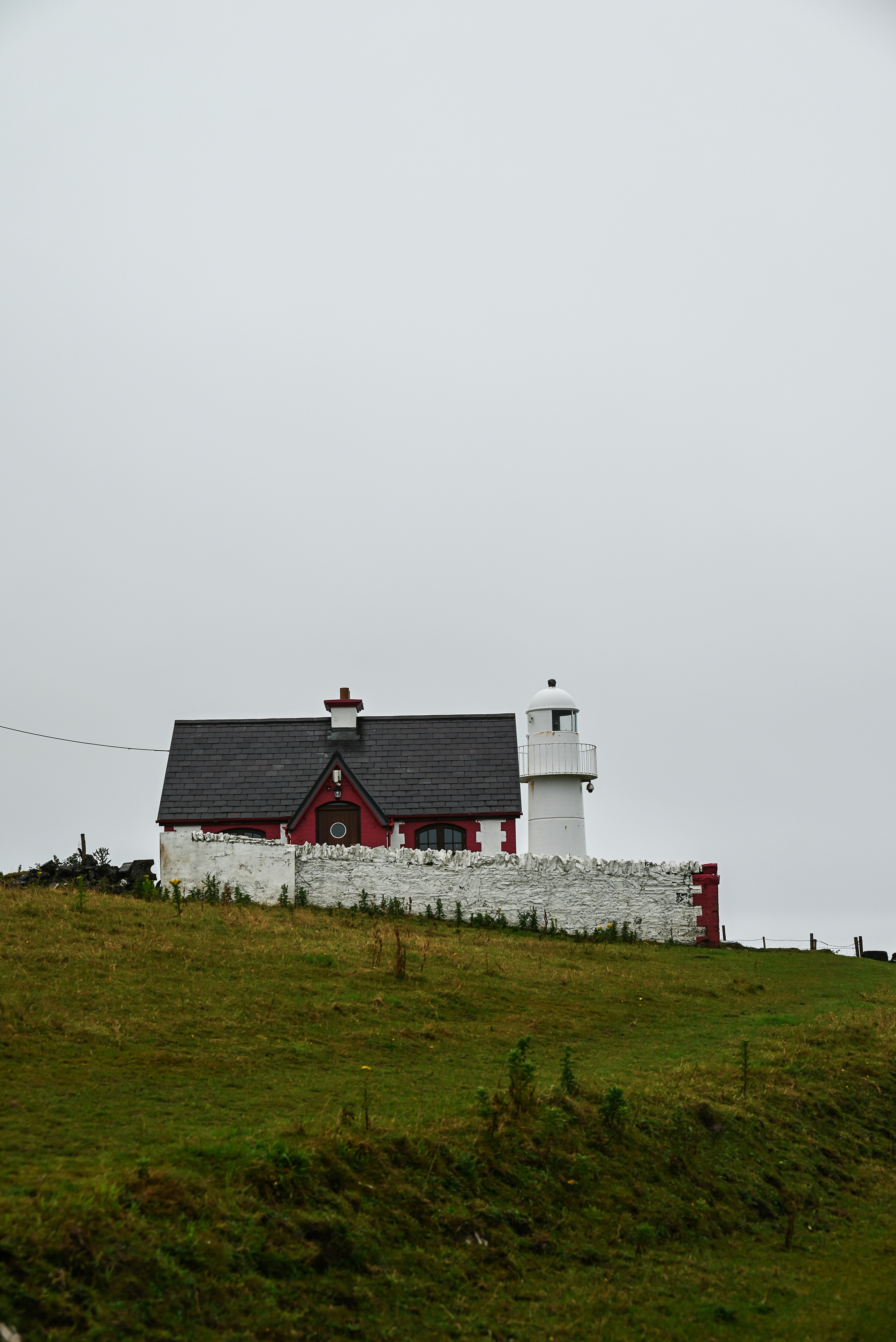 Red-Roofed Cottage and White Lighthouse Standing Guard on a Windswept Hill