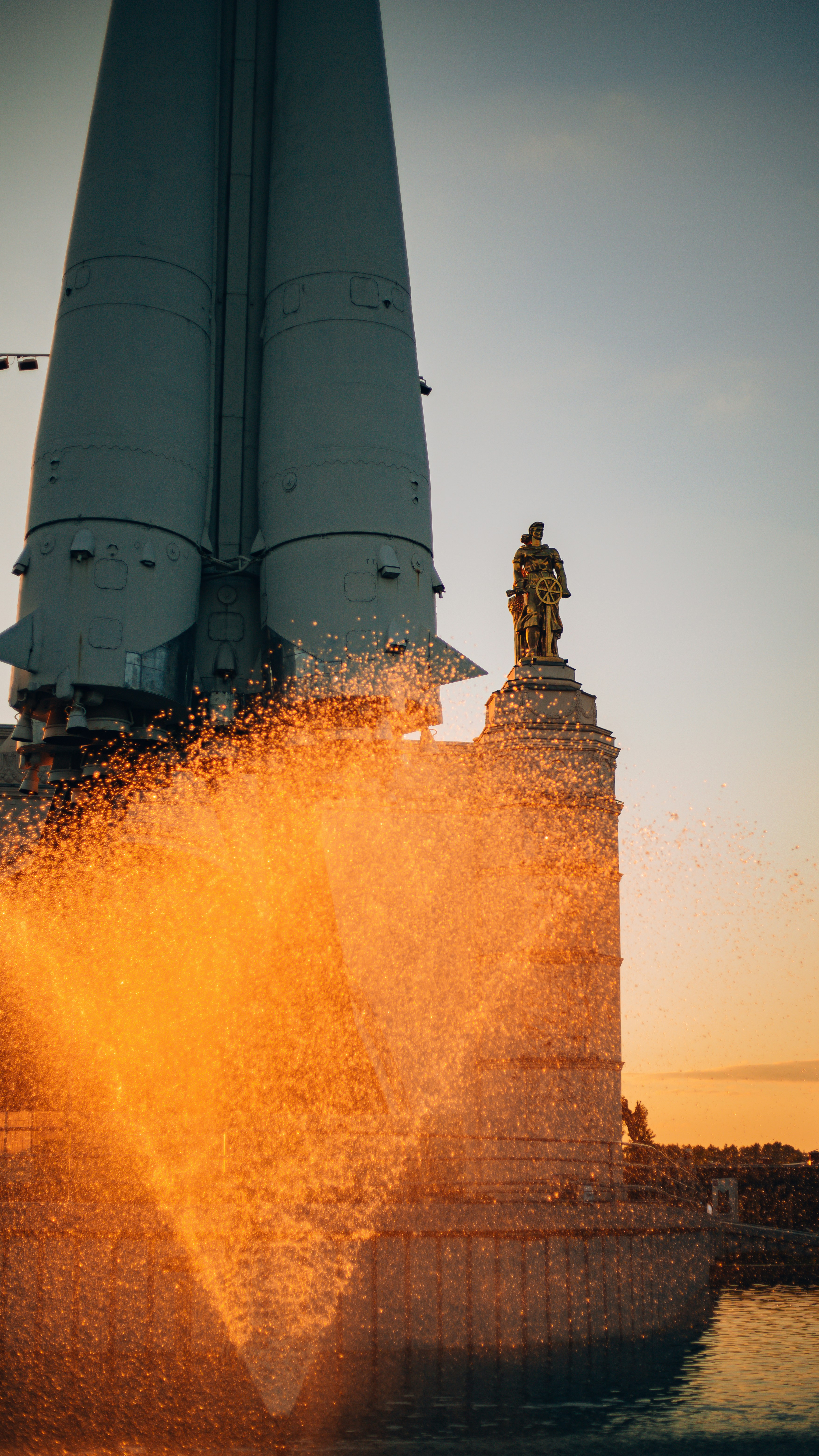 Bronze Sentinel Beside a Teal Rocket Monument, Framed by Sunset Ember