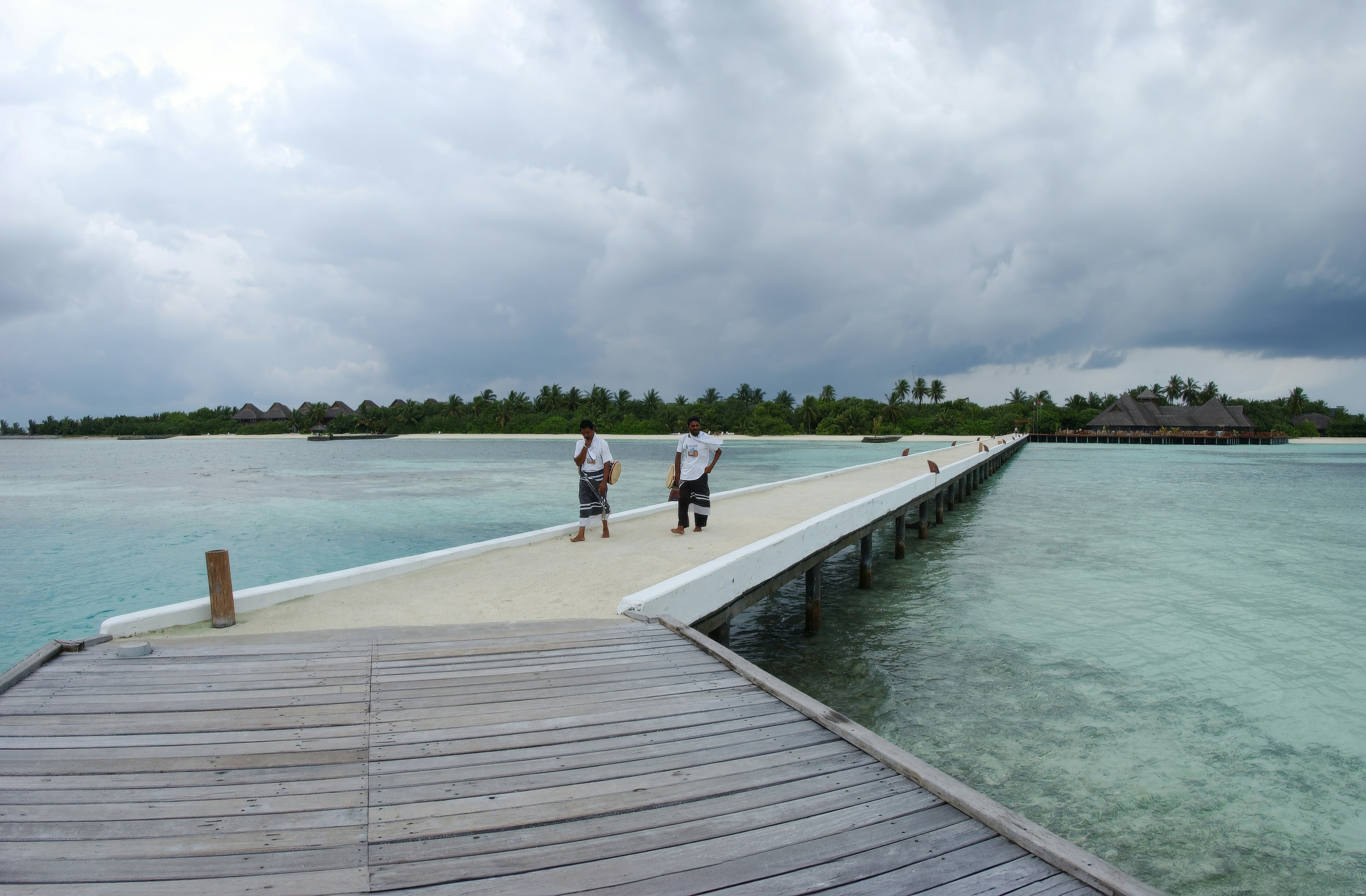 Two Walkers on a Turquoise Pier Under Stormy Skies