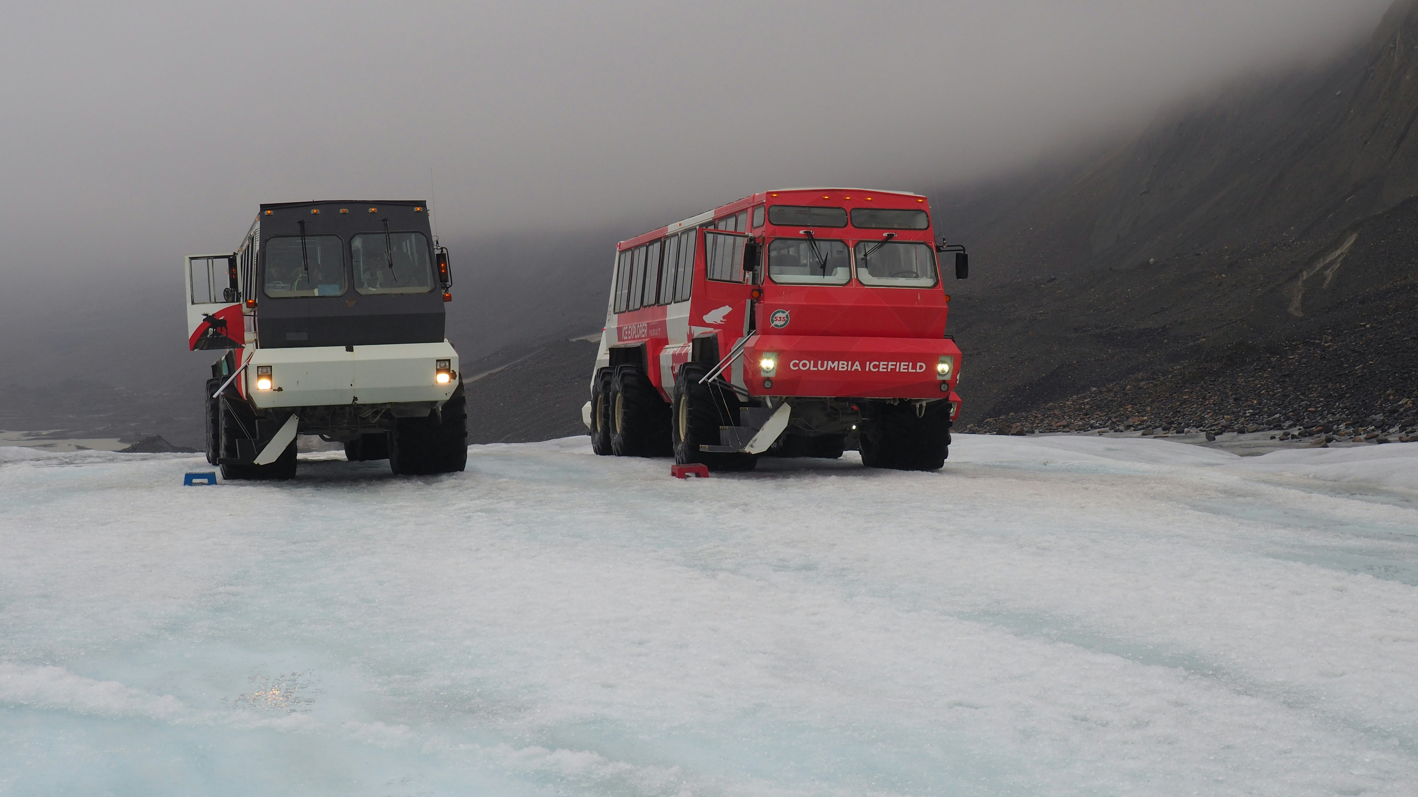 Glacial Convoy: Red and Gray Trucks on a Misty Glacier