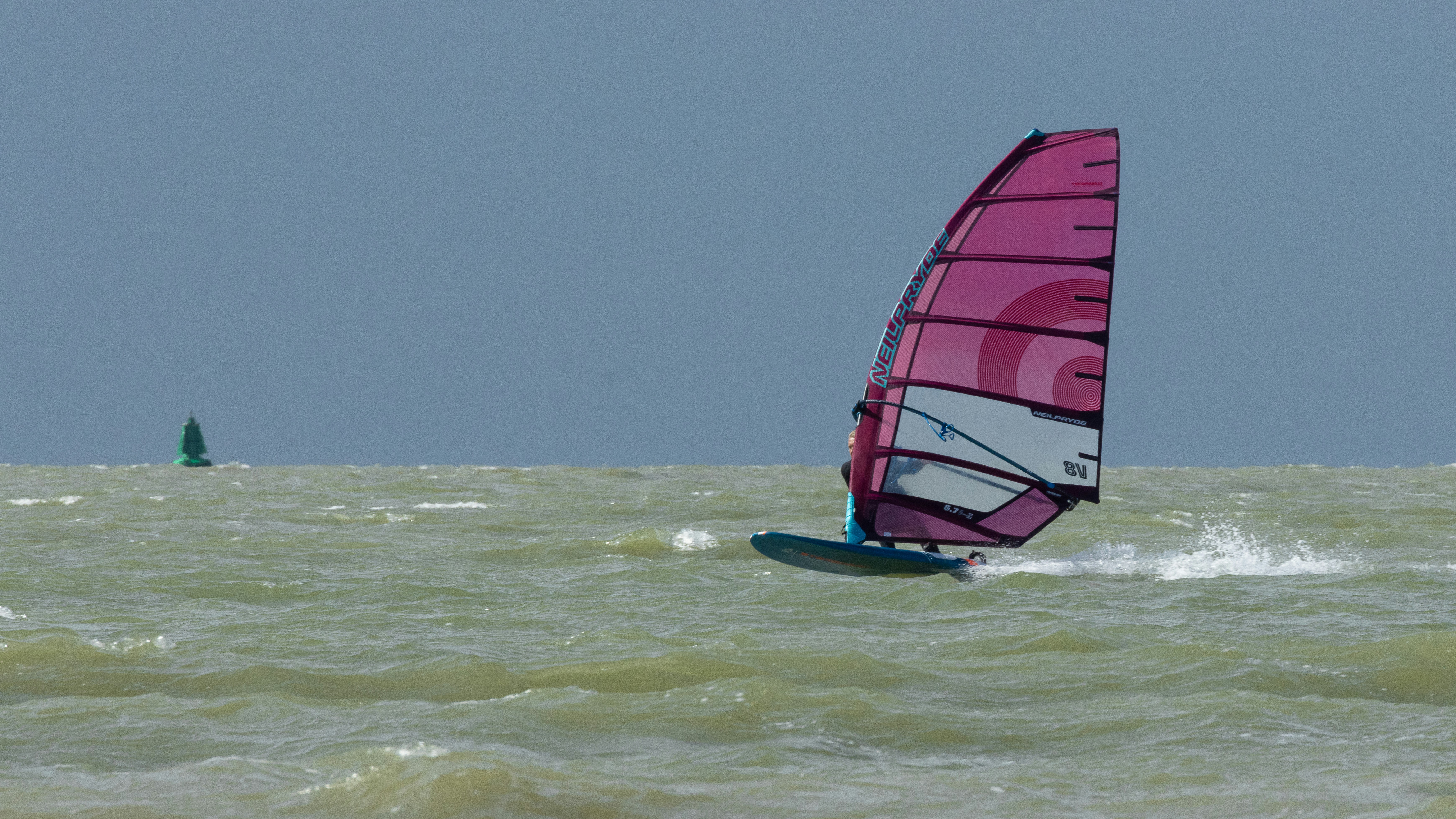 Pink Sails, Emerald Waves: A Windsurfer Cuts Through Choppy Sea