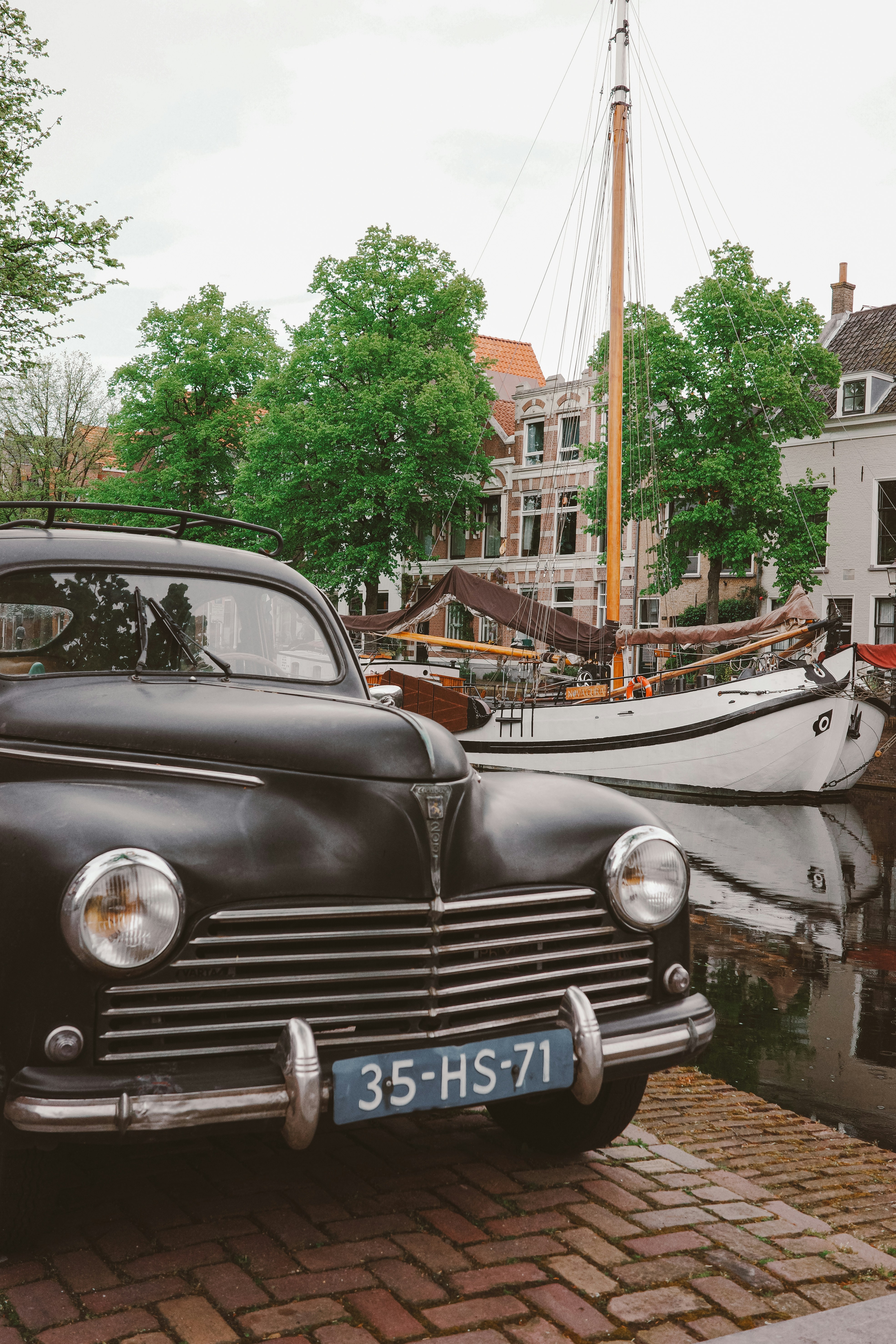 Grille by the Canal: A Vintage Car Meets a Sailboat on a Dutch Quay