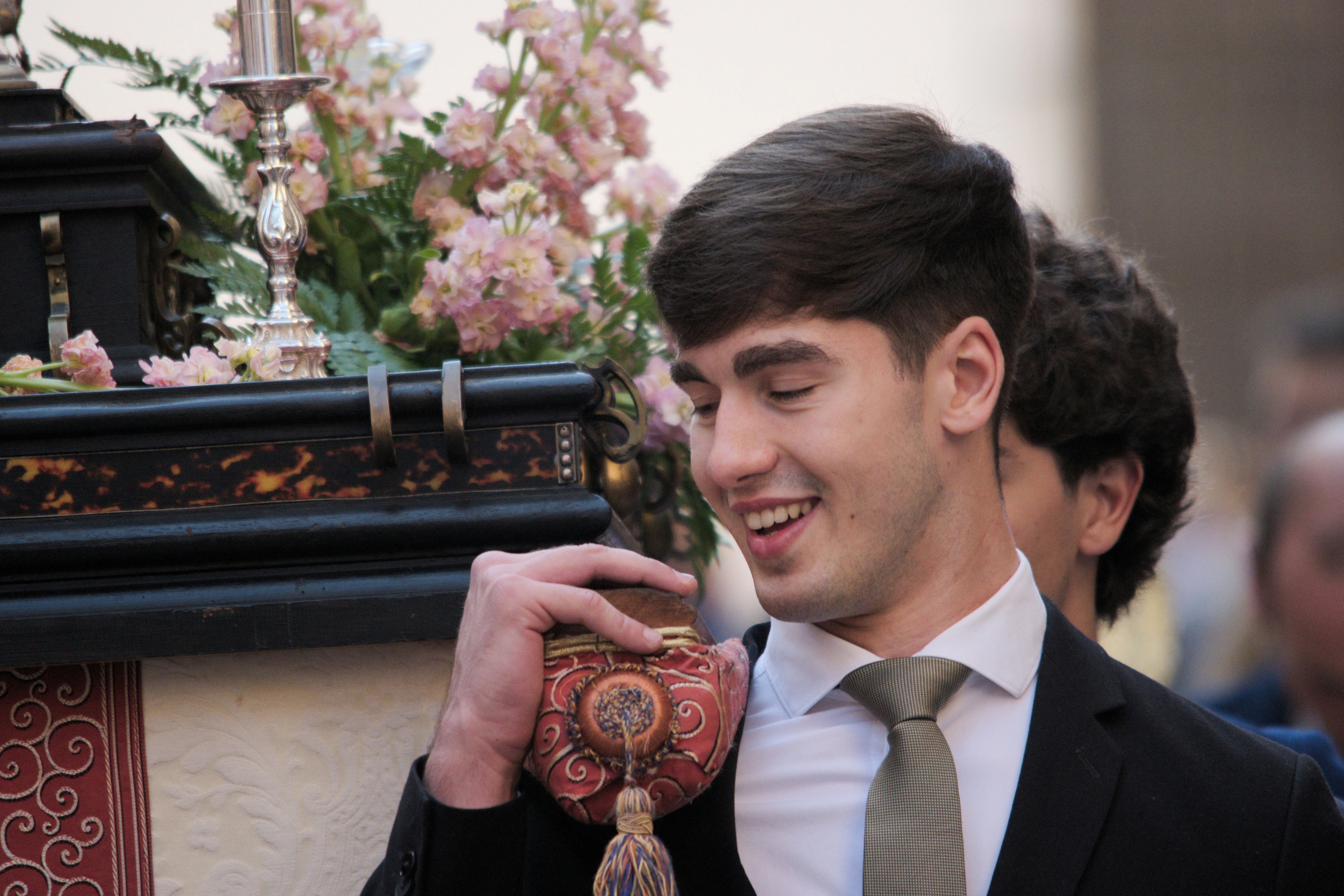 Groom in a Suit Shares a Quiet Smile Next to an Ornate Ceremonial Relic in a Procession
