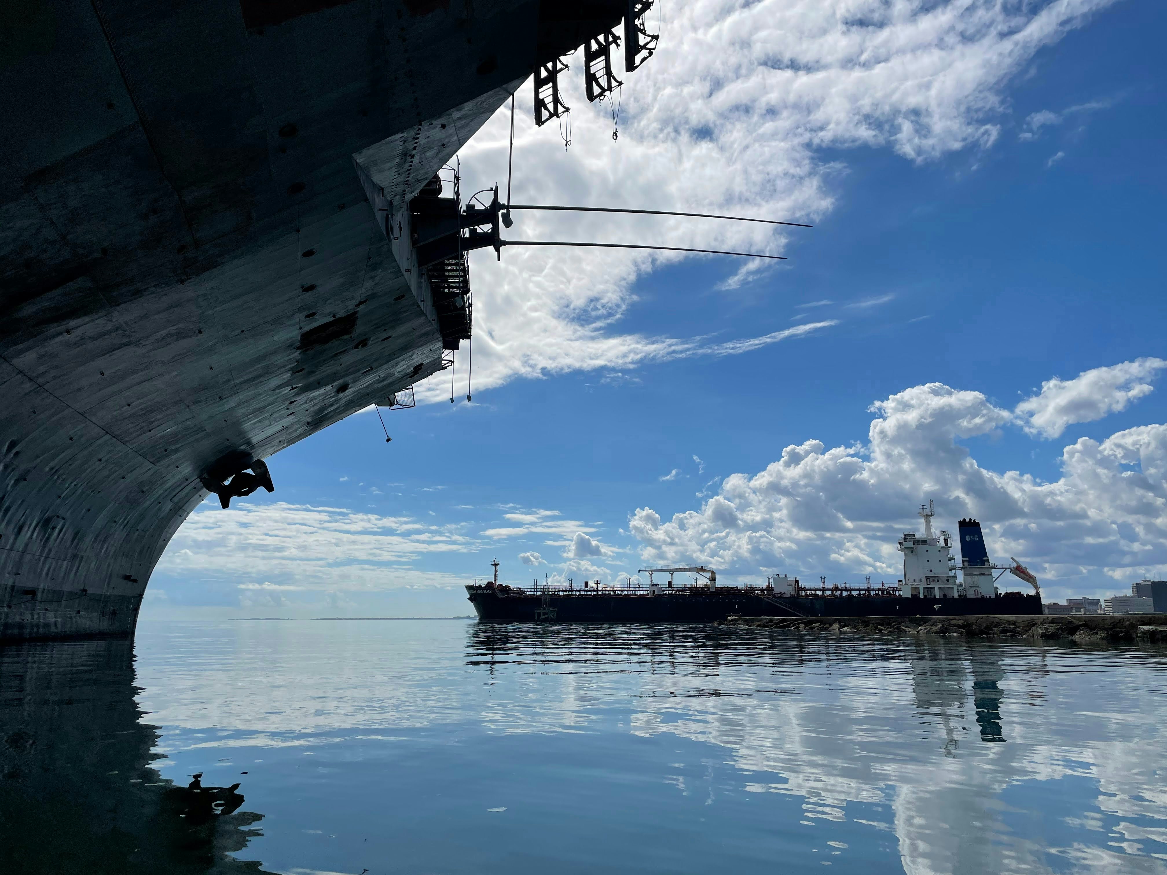 Massive ships docked in calm waters beneath a bright blue sky with scattered clouds.