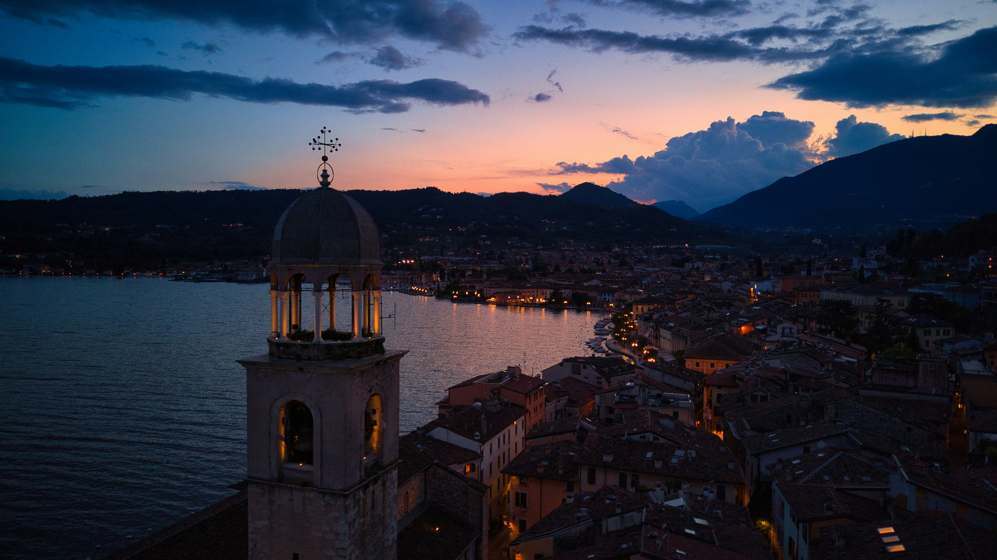 Historic bell tower stands sentinel over the shimmering waters of Lake Como at dusk, with charming village lights twinkling in the background.
