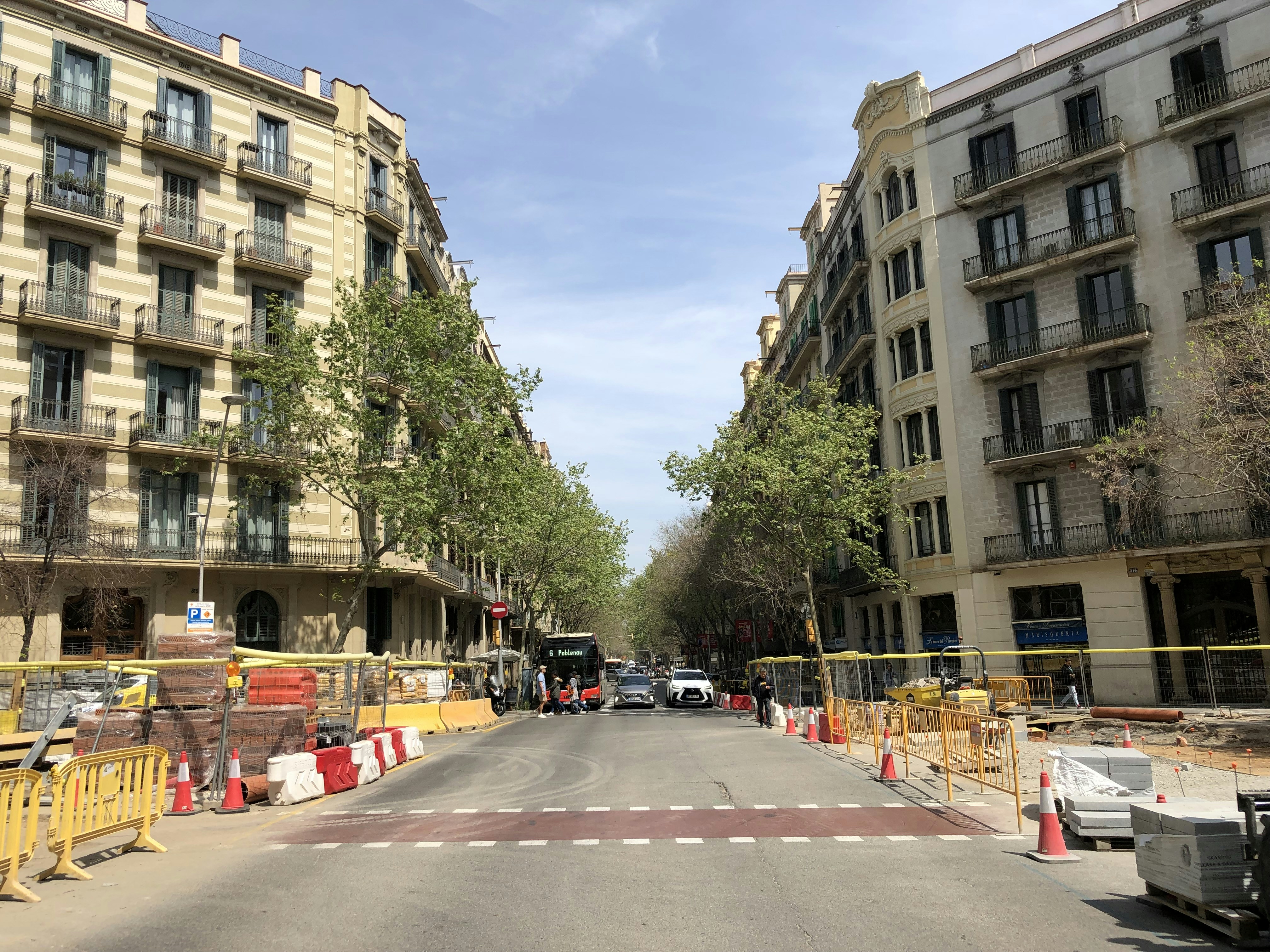 Construction barriers line a city street flanked by classic European buildings under a blue sky.