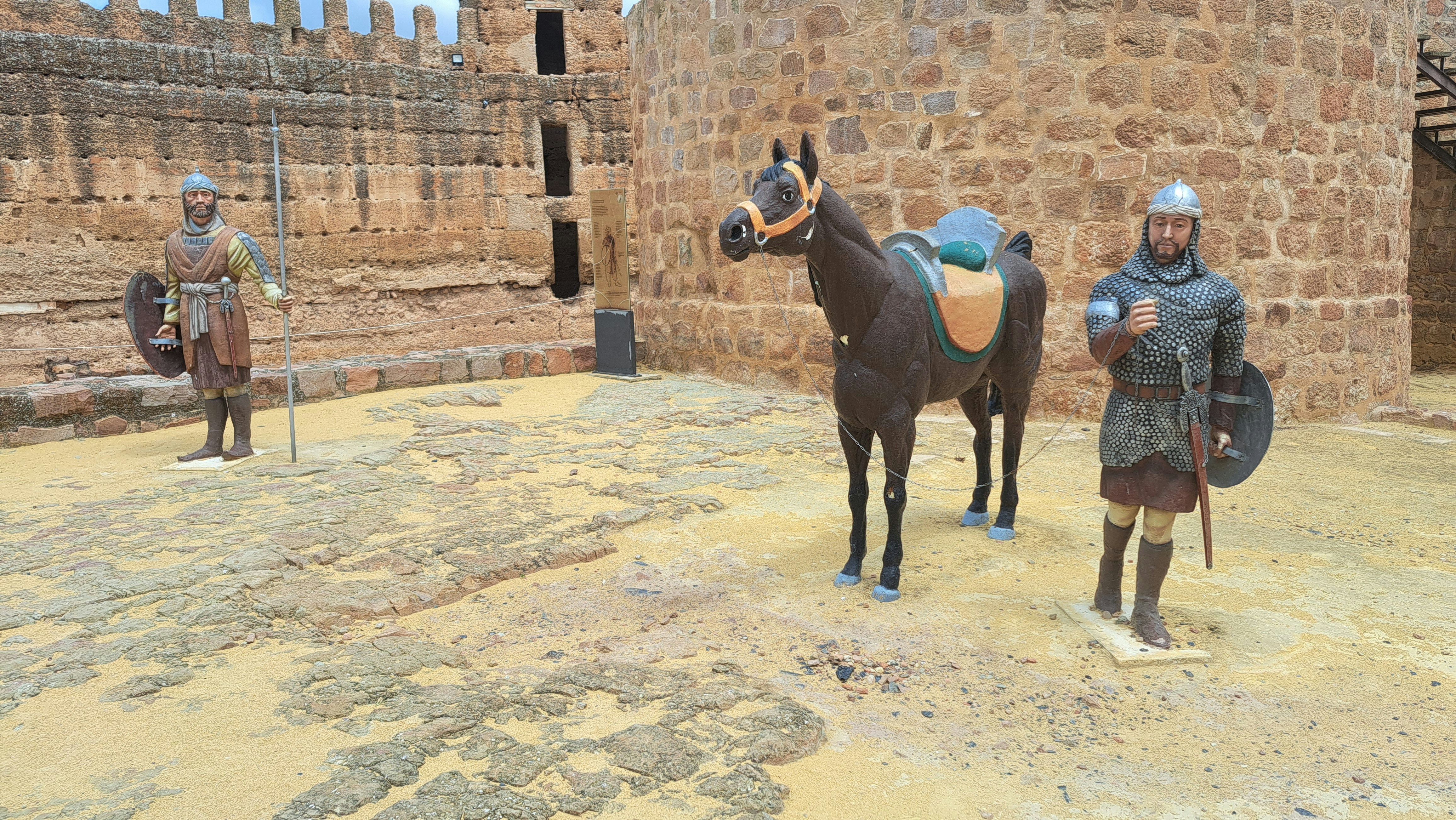 Statues of armored knights and a horse stand in the courtyard of an ancient stone castle.