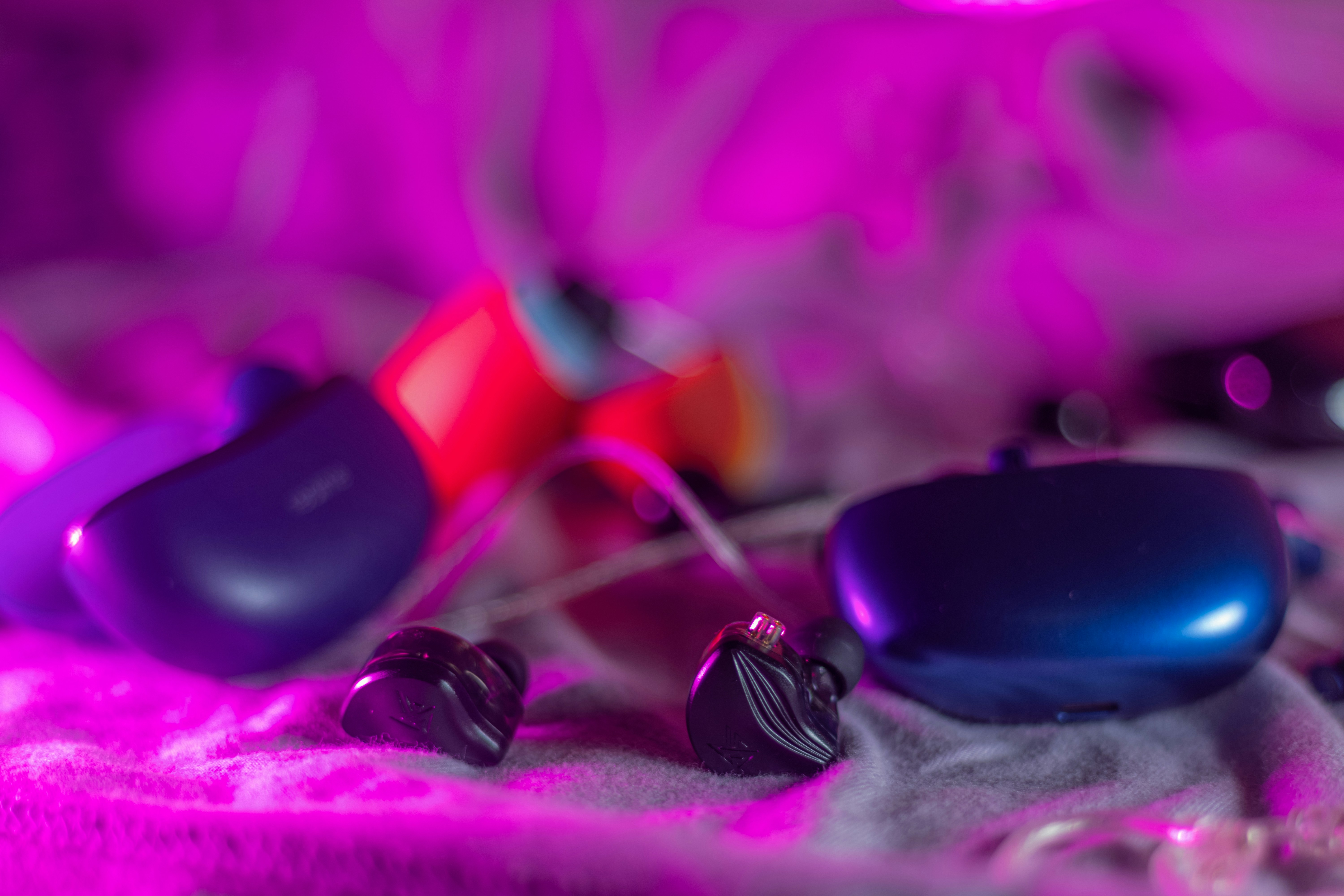 Earbuds resting on a blanket illuminated by a vibrant purple and blue light.