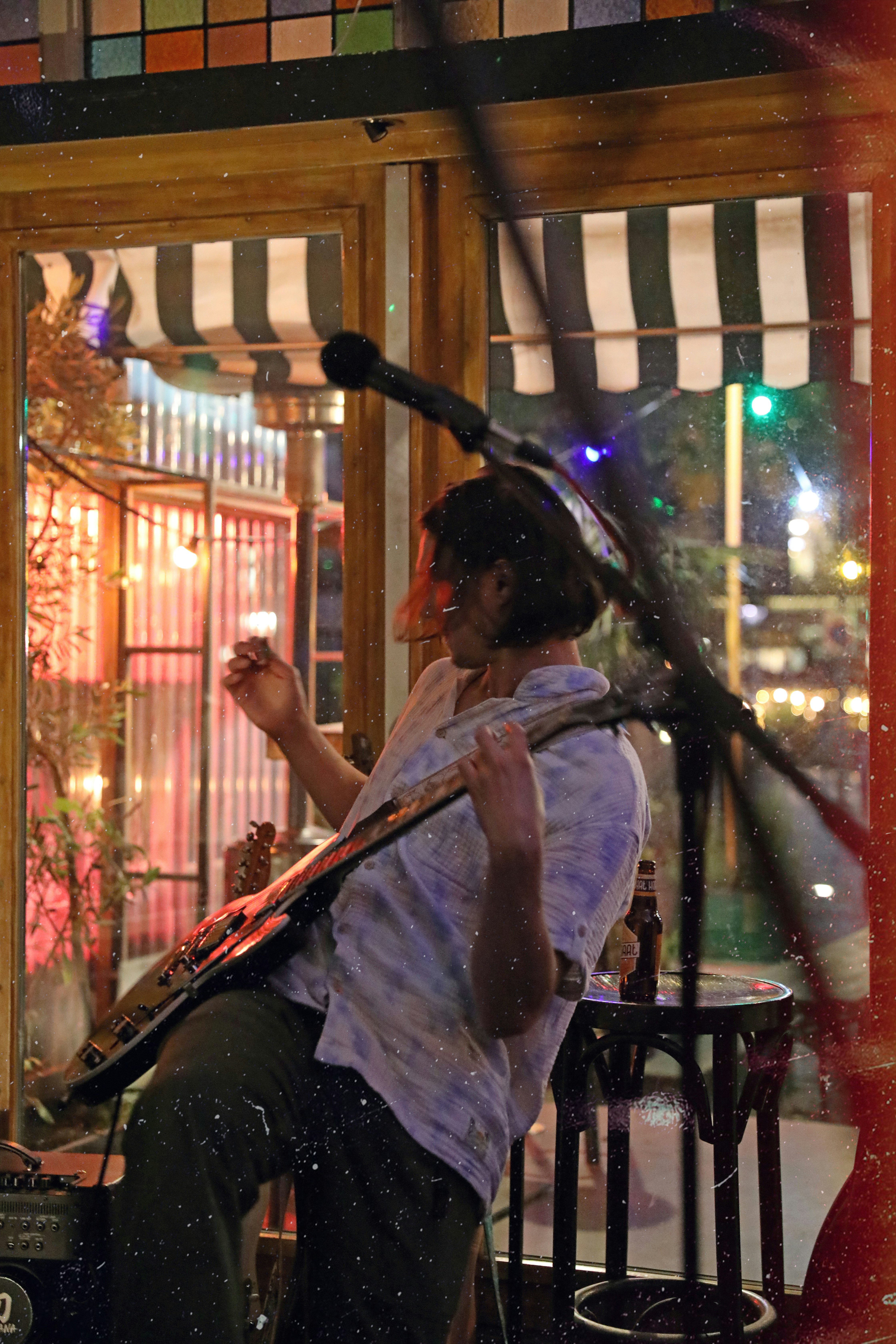 Neon Serenade Through Glass: A Guitarist in a Nighttime Café