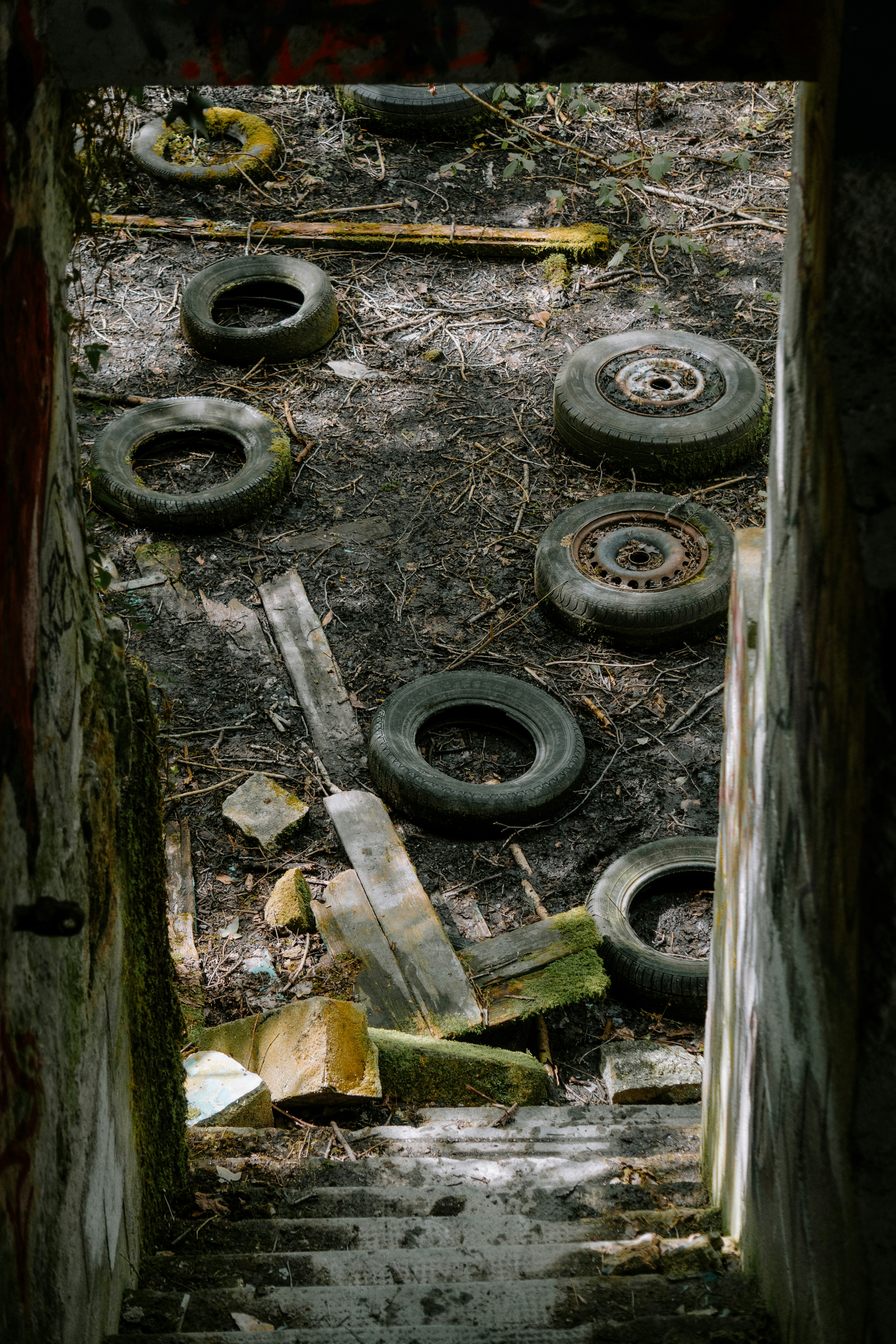 Overgrown staircase leading down to a scattered collection of old tires and debris in a neglected area. 
