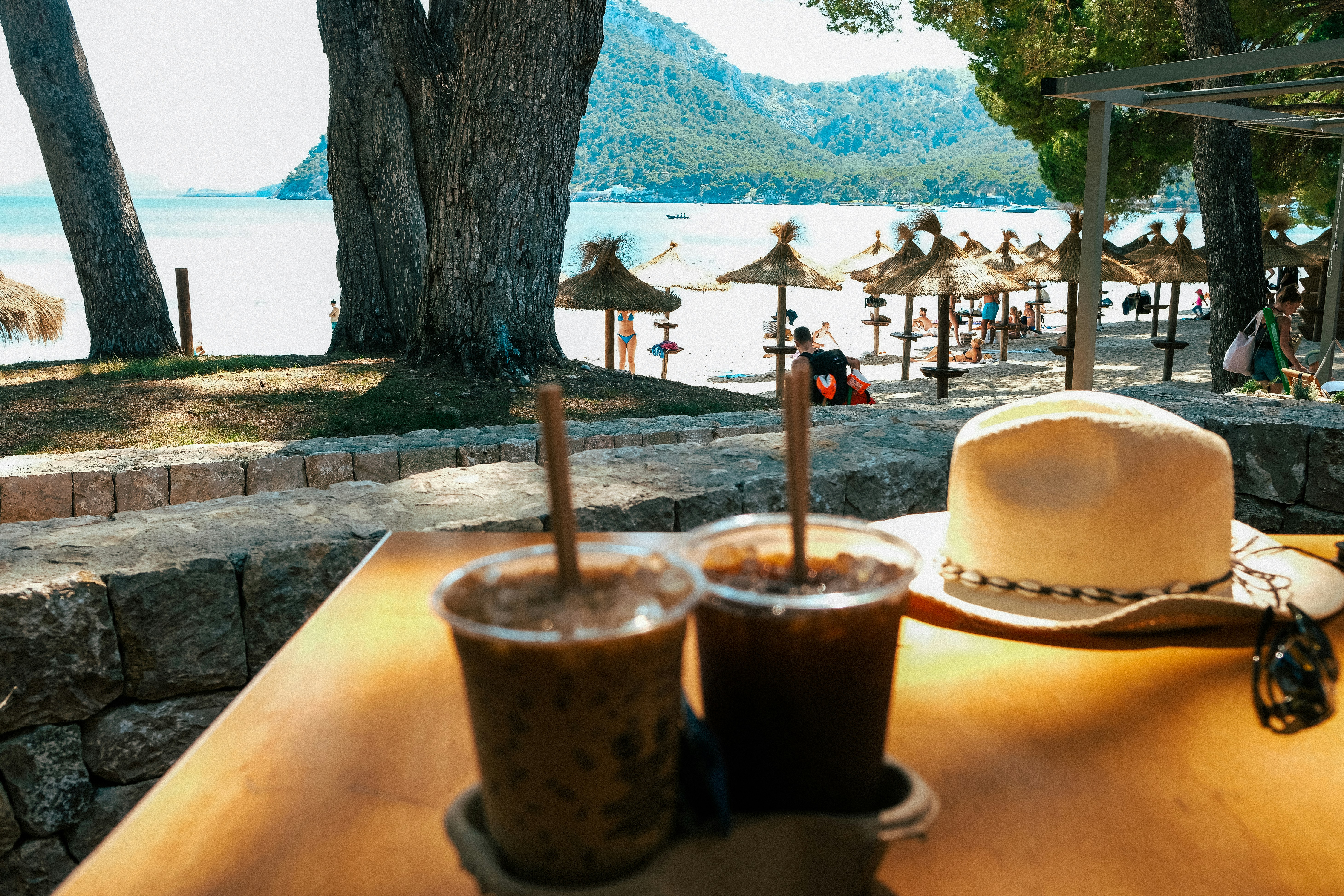 Sunlit Shore Table: Iced Drinks, a Straw Hat, and a Calm Sea View
