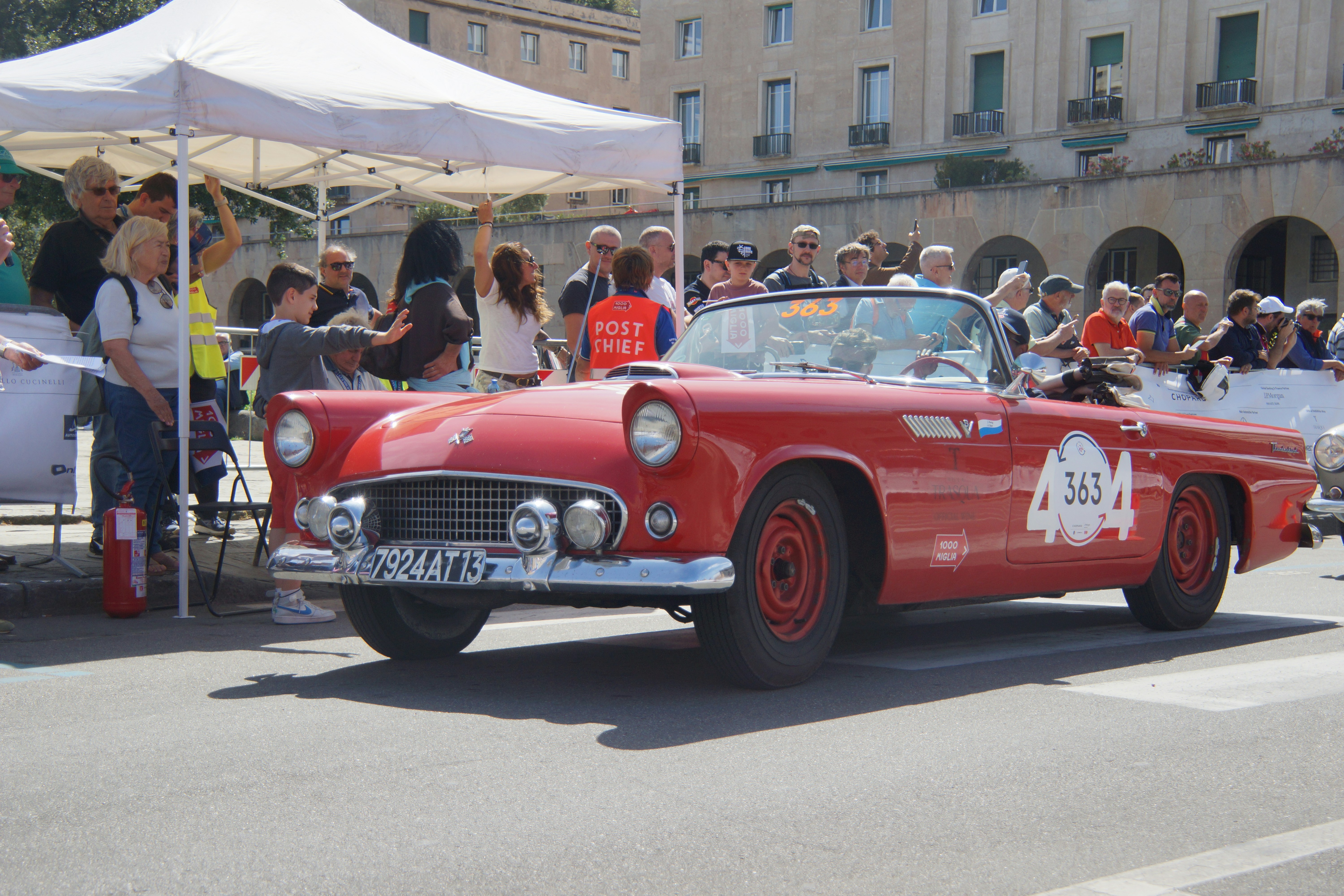 A red car driving down a street past a crowd of people photo – Free Car ...
