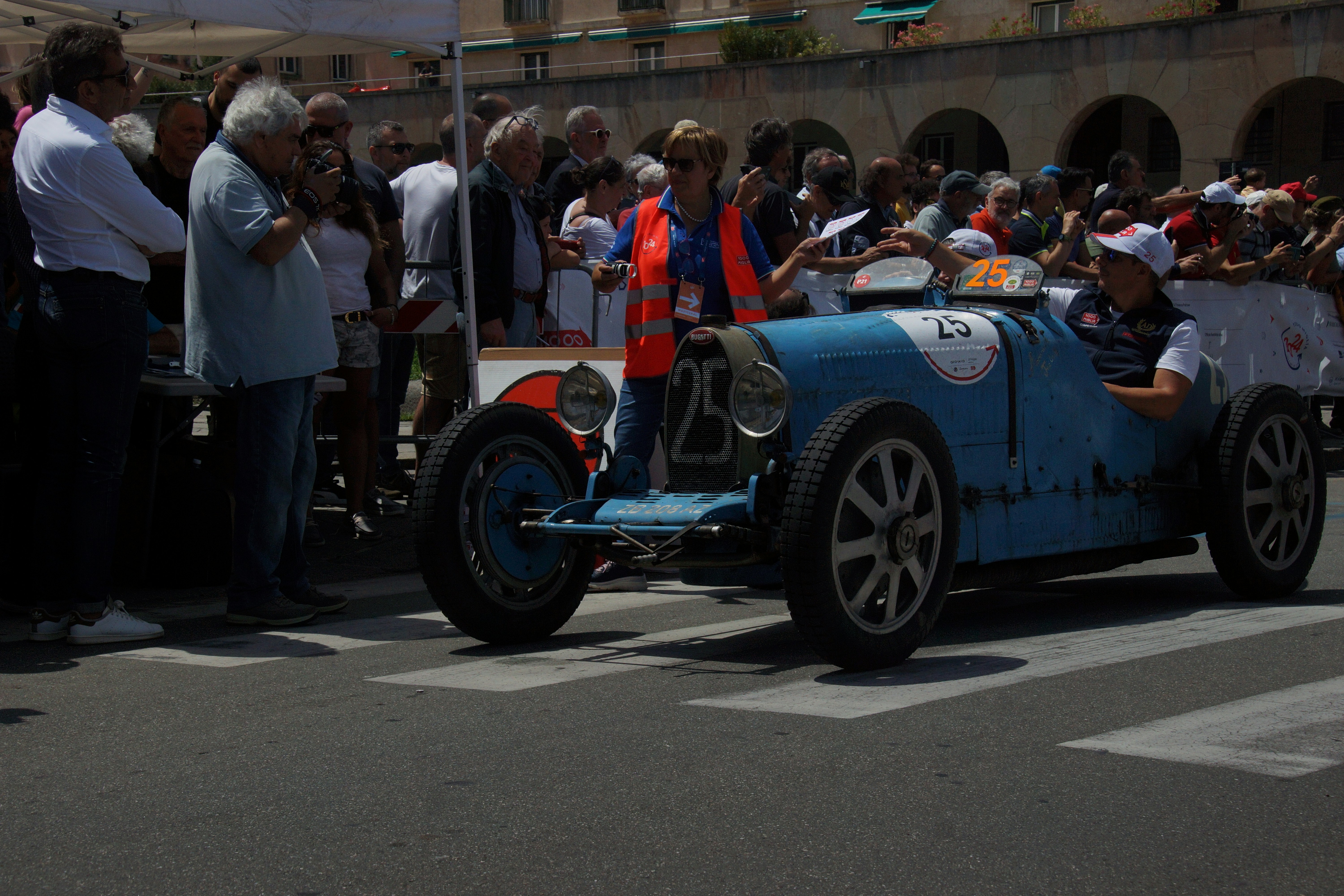 A blue race car driving down a street past a crowd of people photo ...
