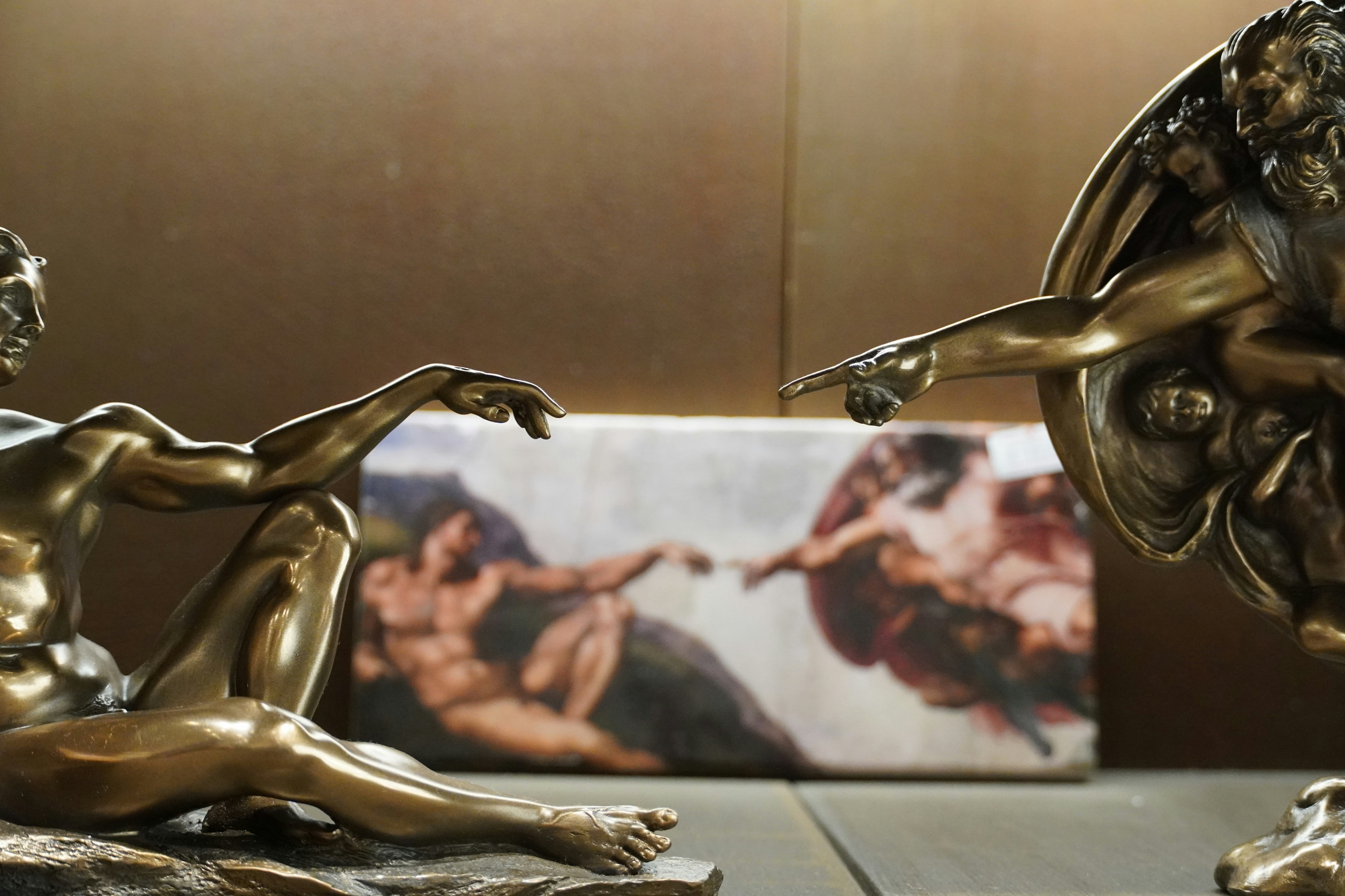 Bronze sculptures depicting a moment of divine interaction, with one figure reaching out while the other gestures emphatically, set against a backdrop of classical art.
