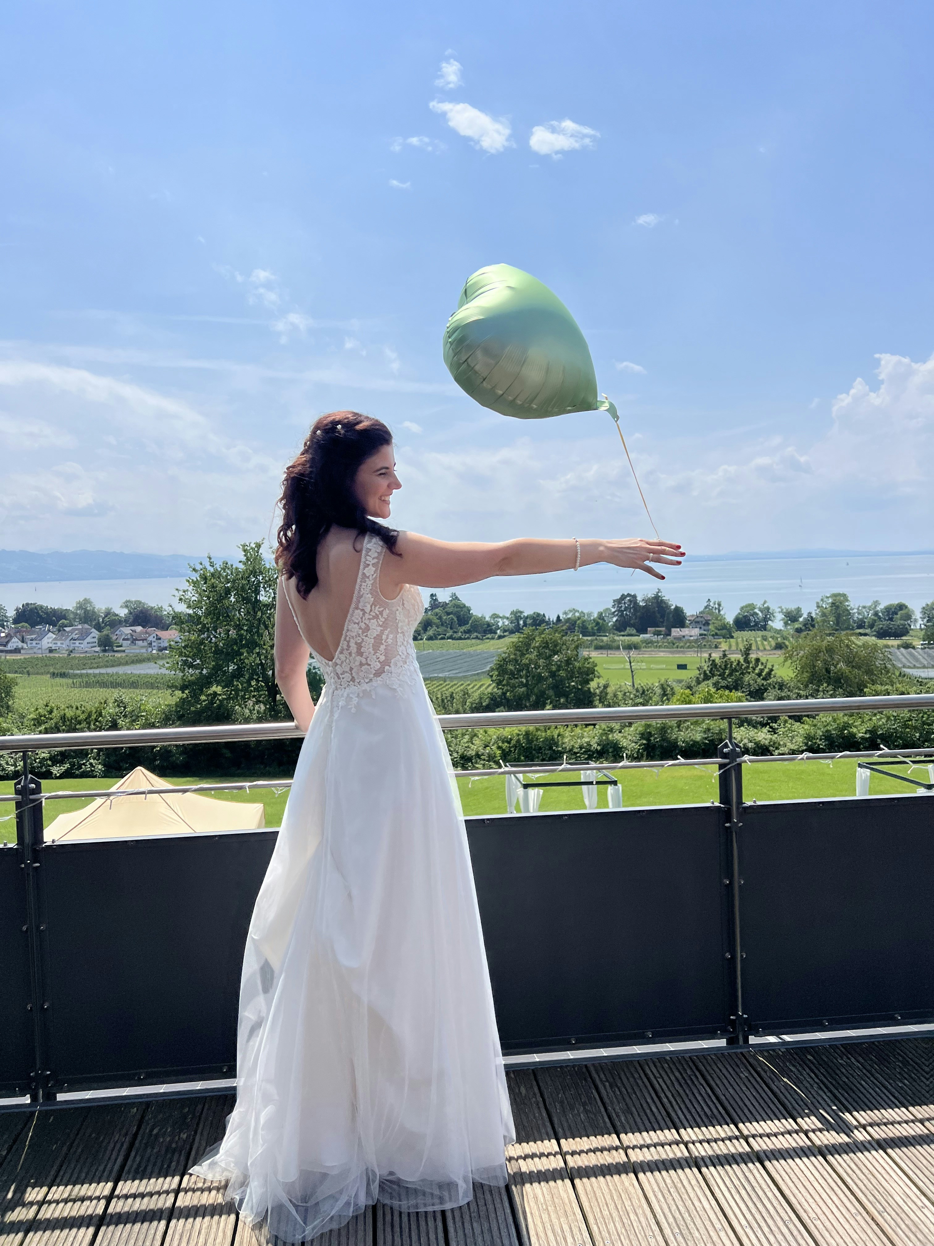 Bride with teal balloon on a sunlit balcony overlooking a coastal valley