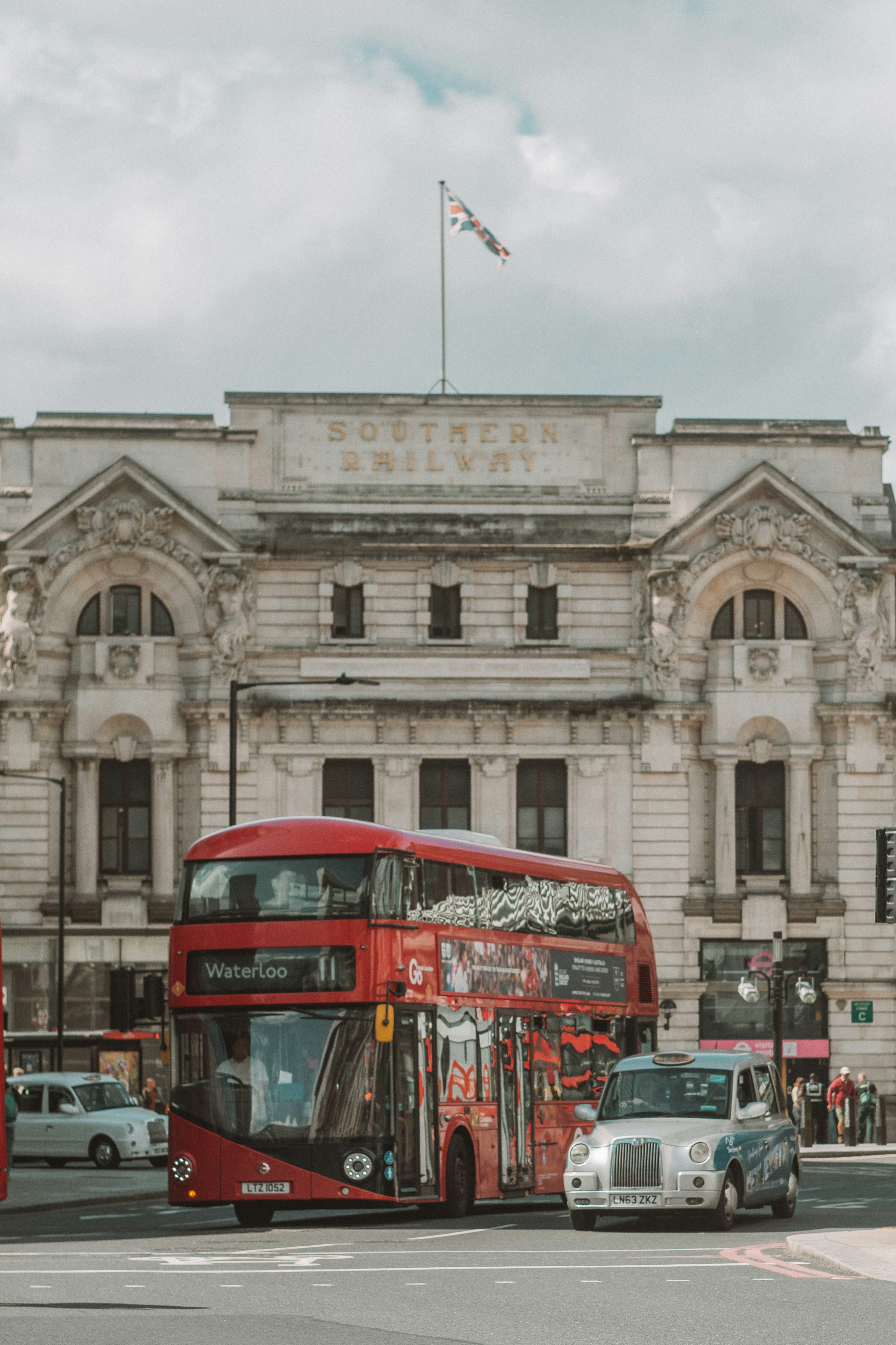 A red double decker bus driving past a tall building photo – Free ...