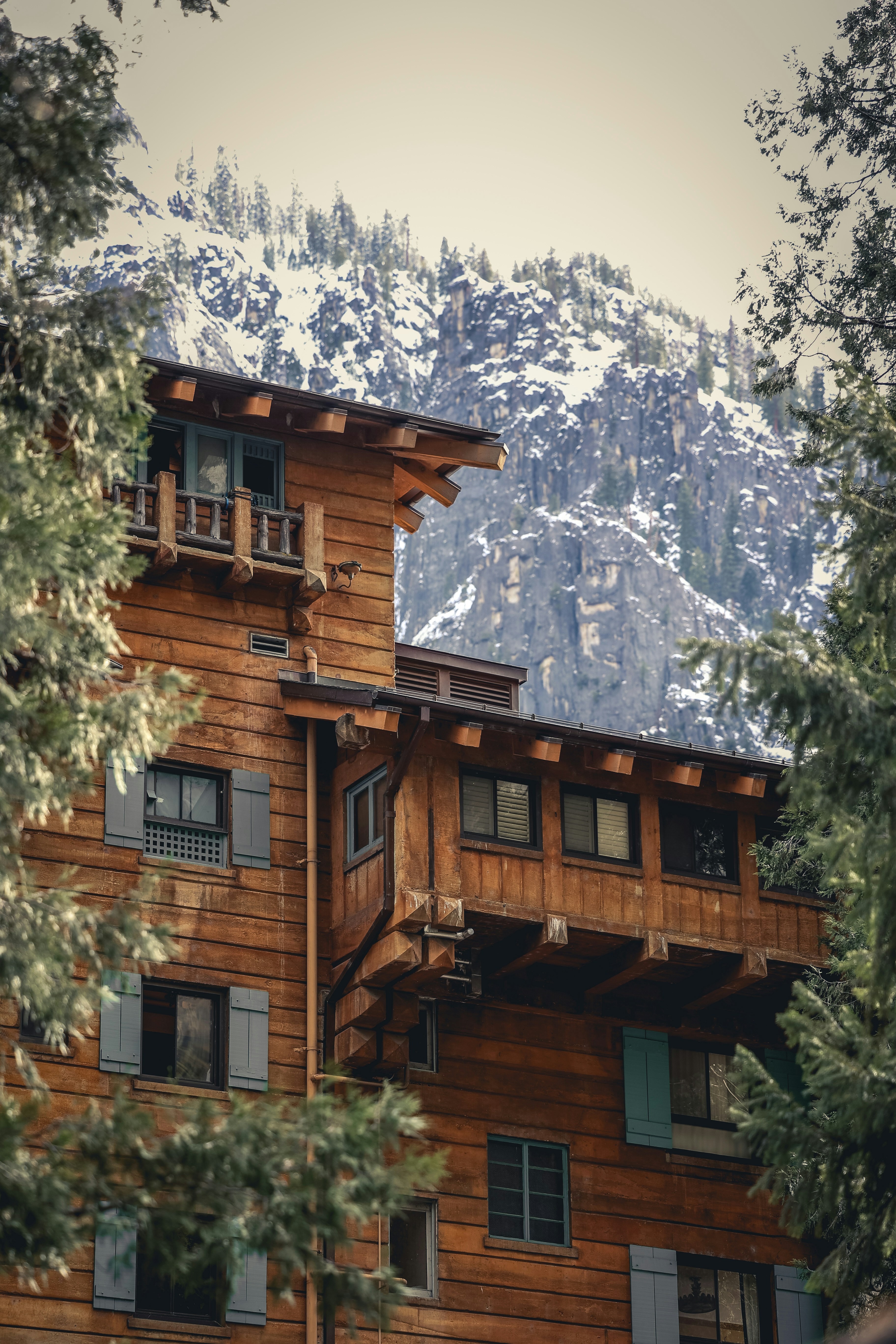 Rustic wooden lodge nestled among evergreen trees, with snow-capped mountains in the background.