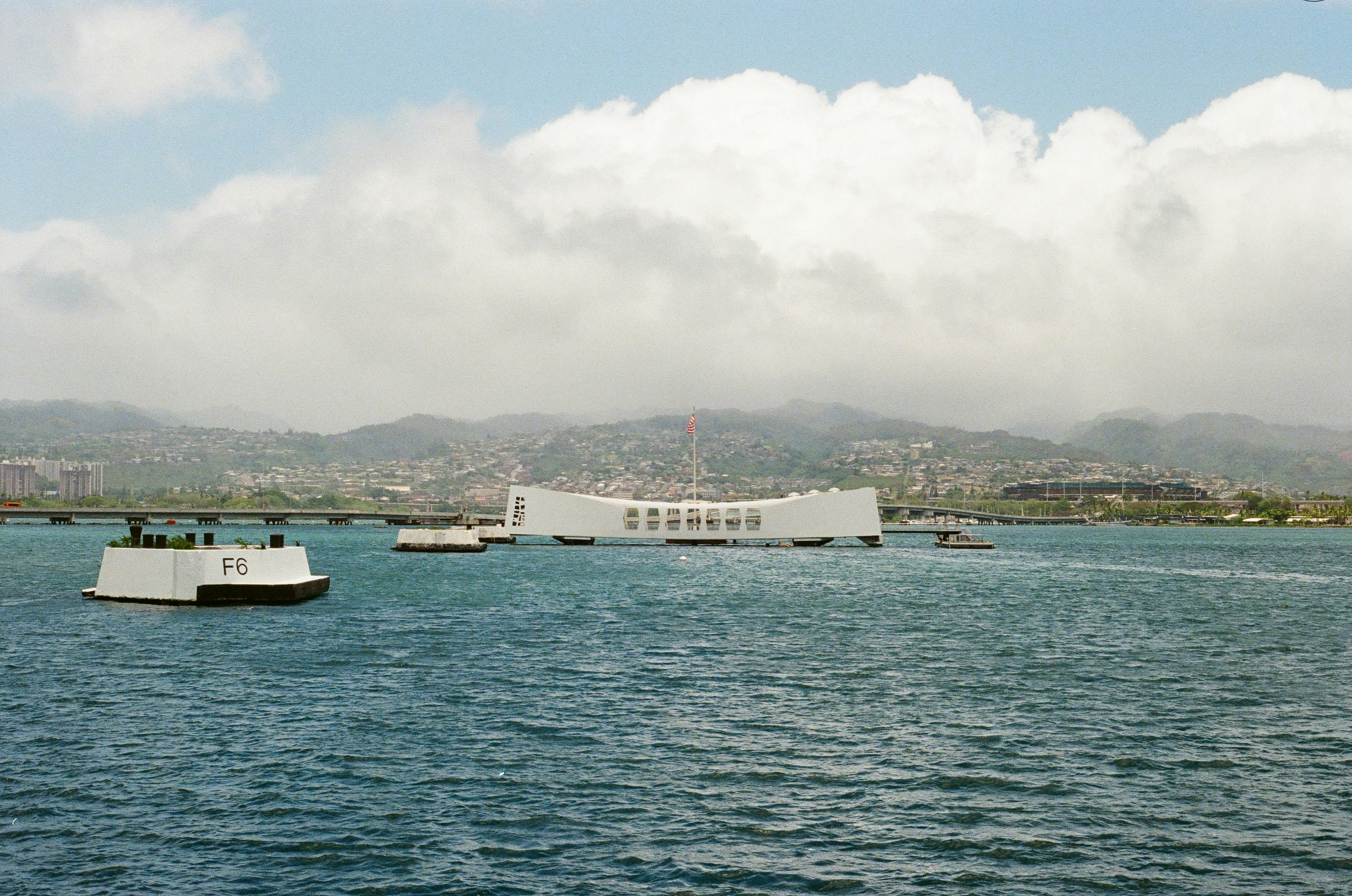 USS Arizona Memorial rising above the waters in Pearl Harbor, surrounded by a serene landscape and distant hills. A poignant reminder of a significant historical event.