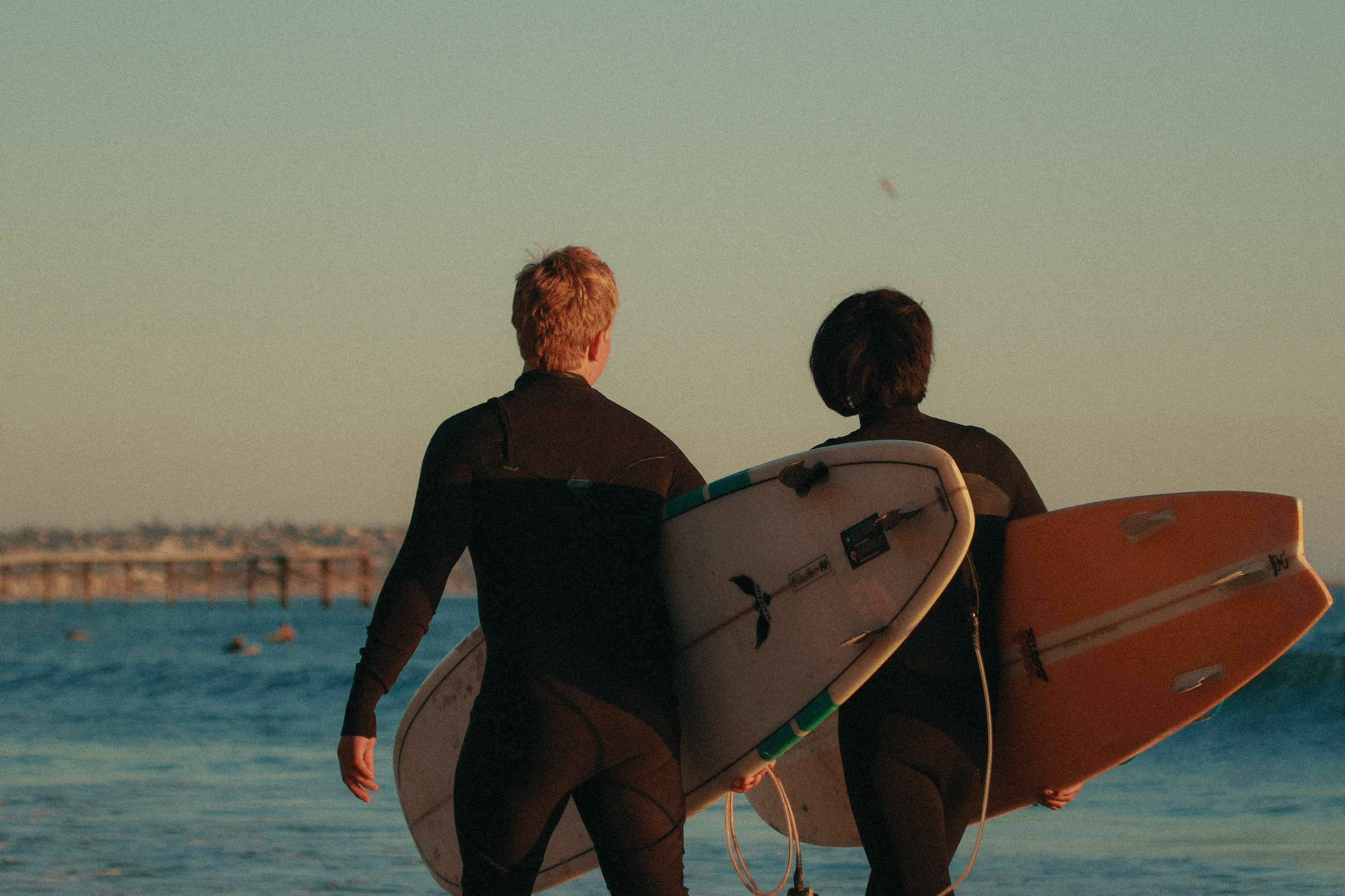 Dusk Glare and Two Silhouettes: Surfers Walk Toward the Sea