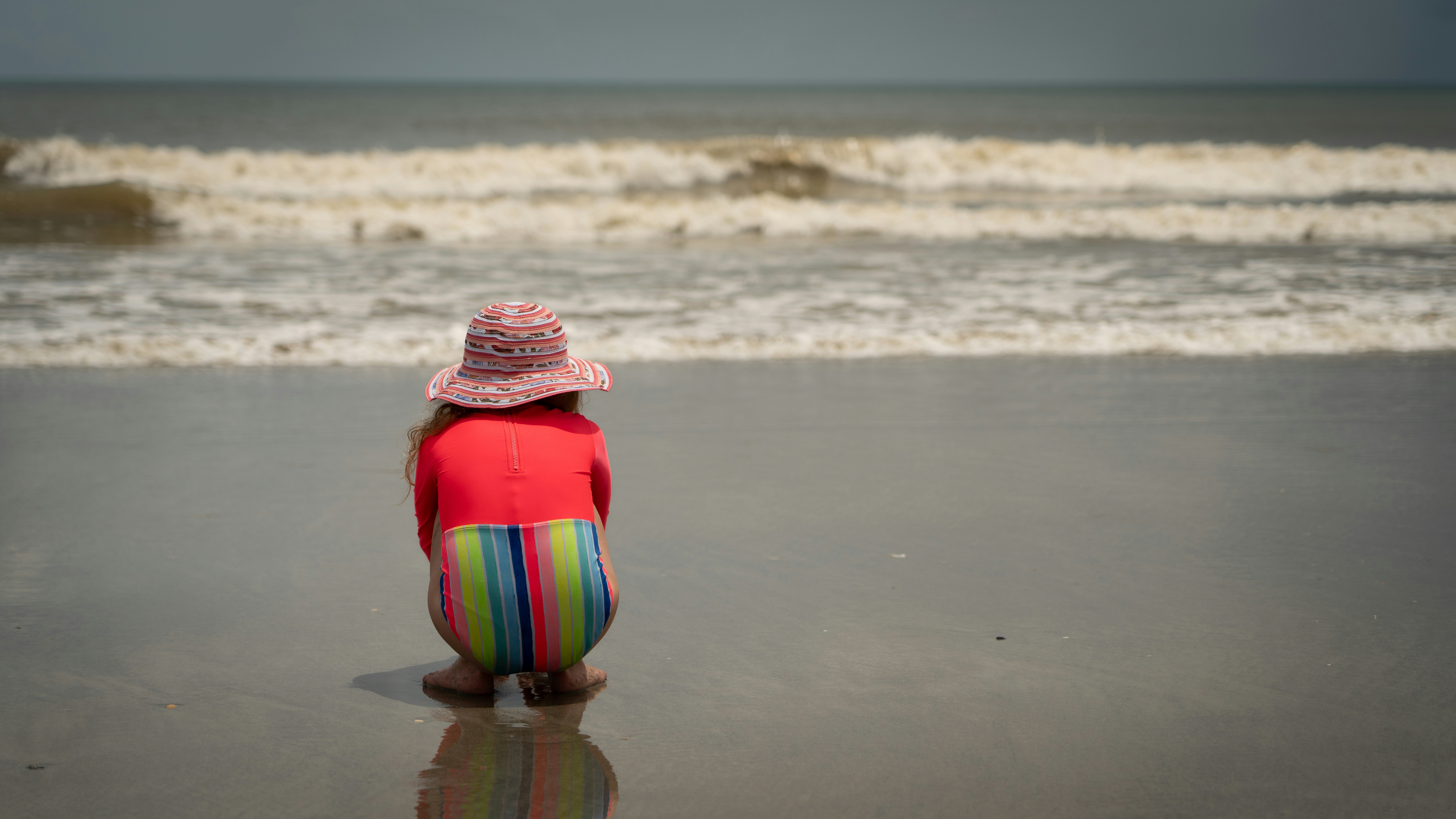a little girl sitting on top of a beach next to the ocean