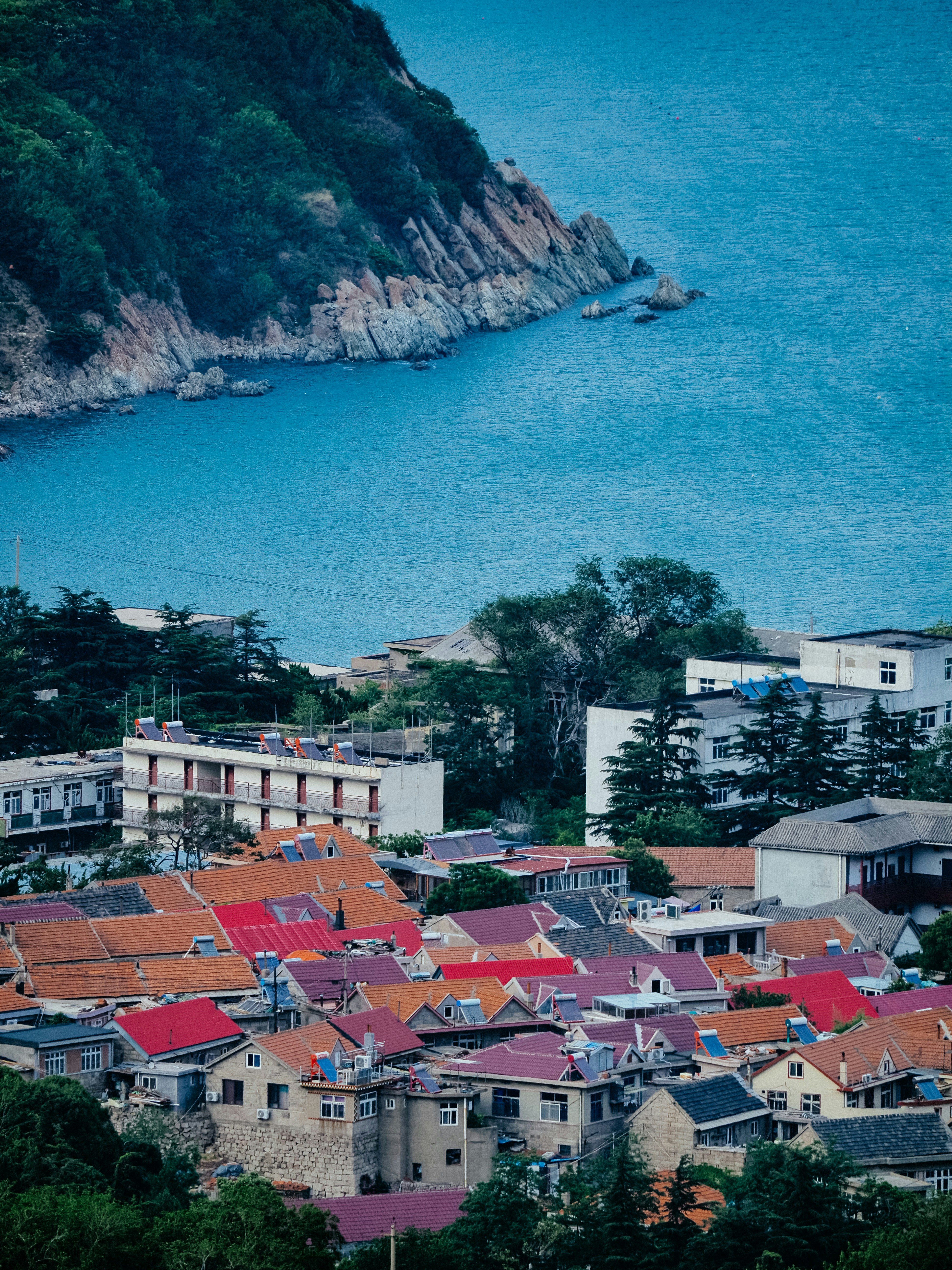 Colorful rooftops of a coastal village nestled against a backdrop of rocky cliffs and serene blue waters.