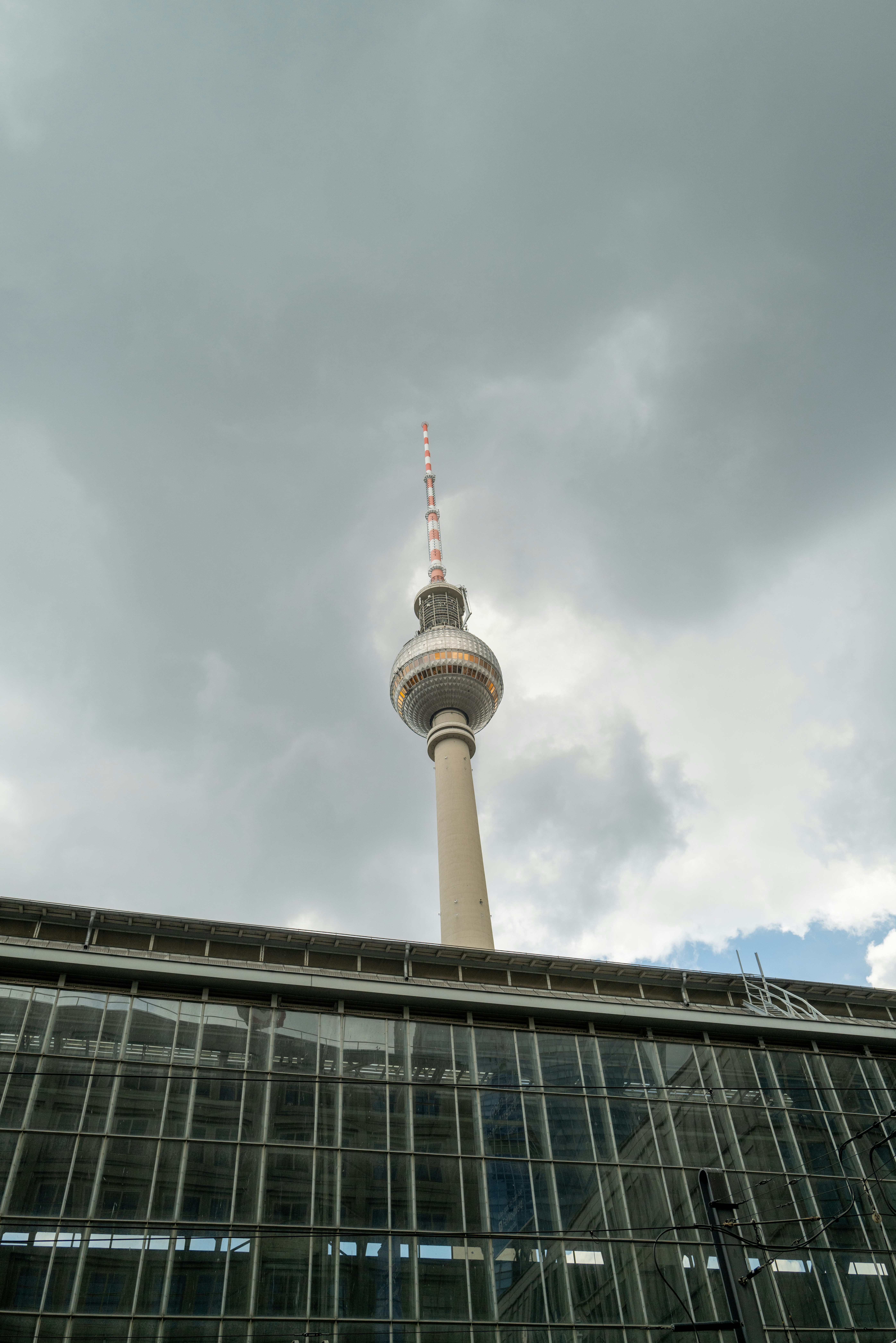 Berlin’s Fernsehturm Pierces a Cloudy Skyline Over a Glass Facade