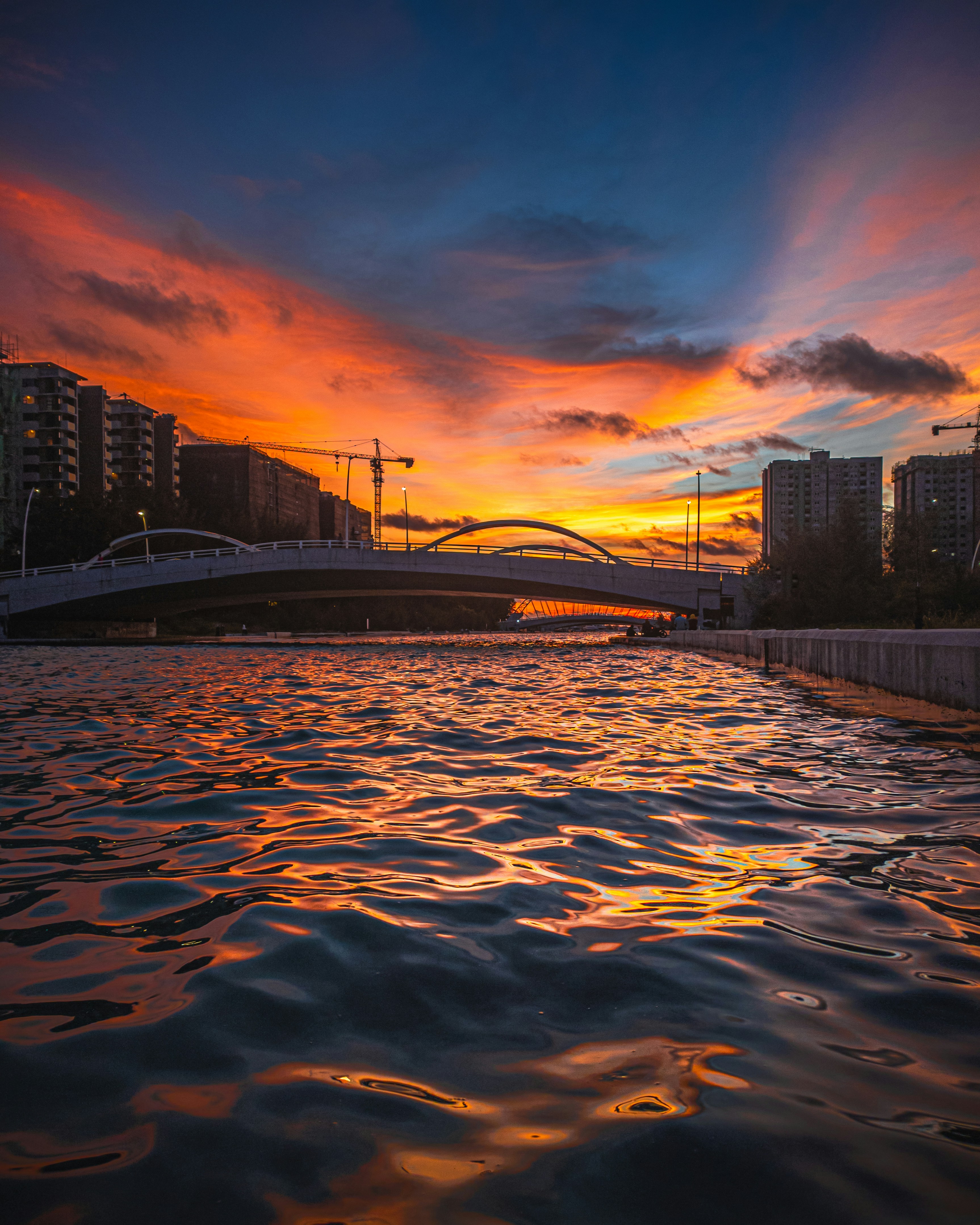 the sun is setting over the water with a bridge in the background