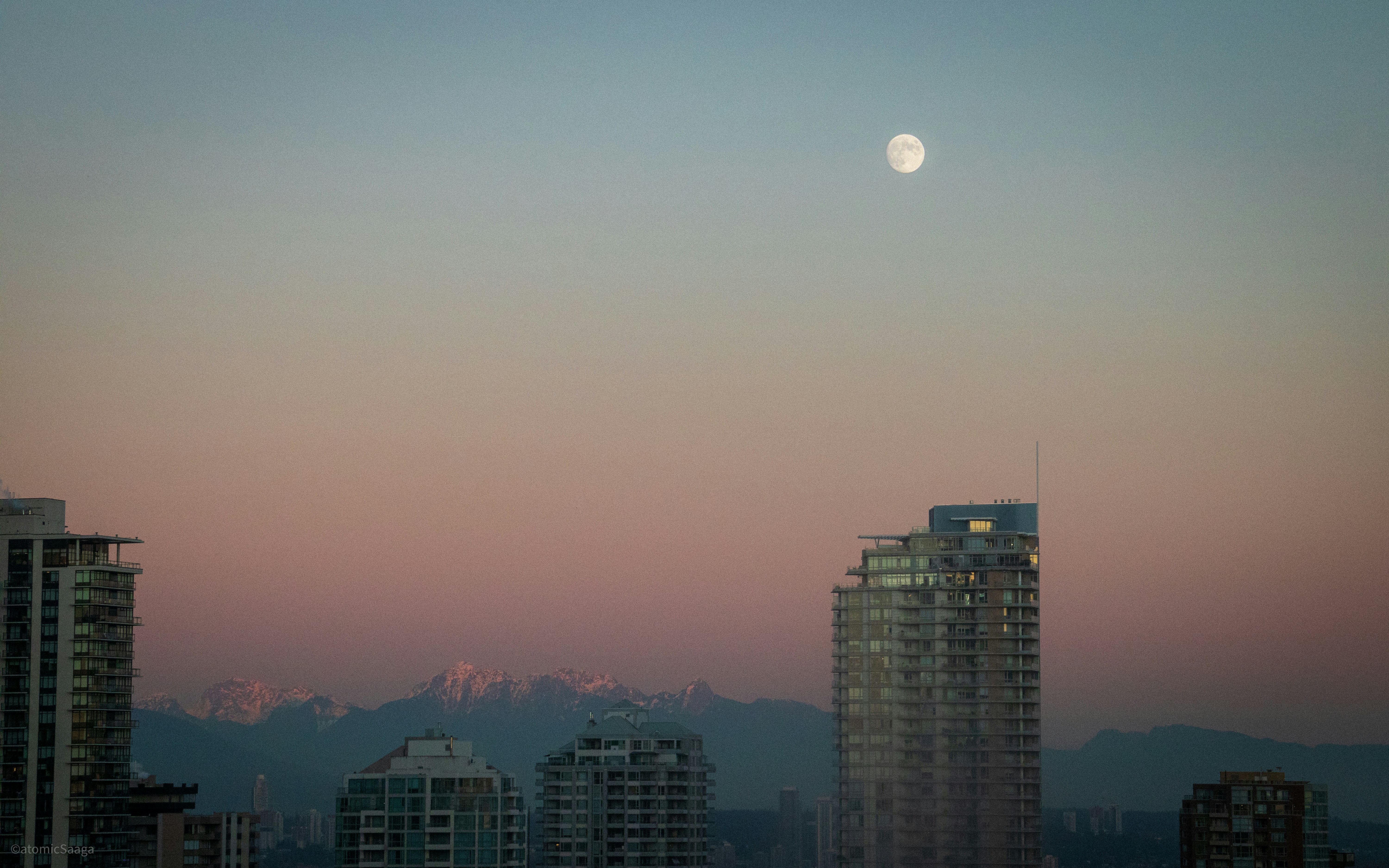 Moon Over a Quiet City Skyline at Dusk, with Snow-Capped Peaks