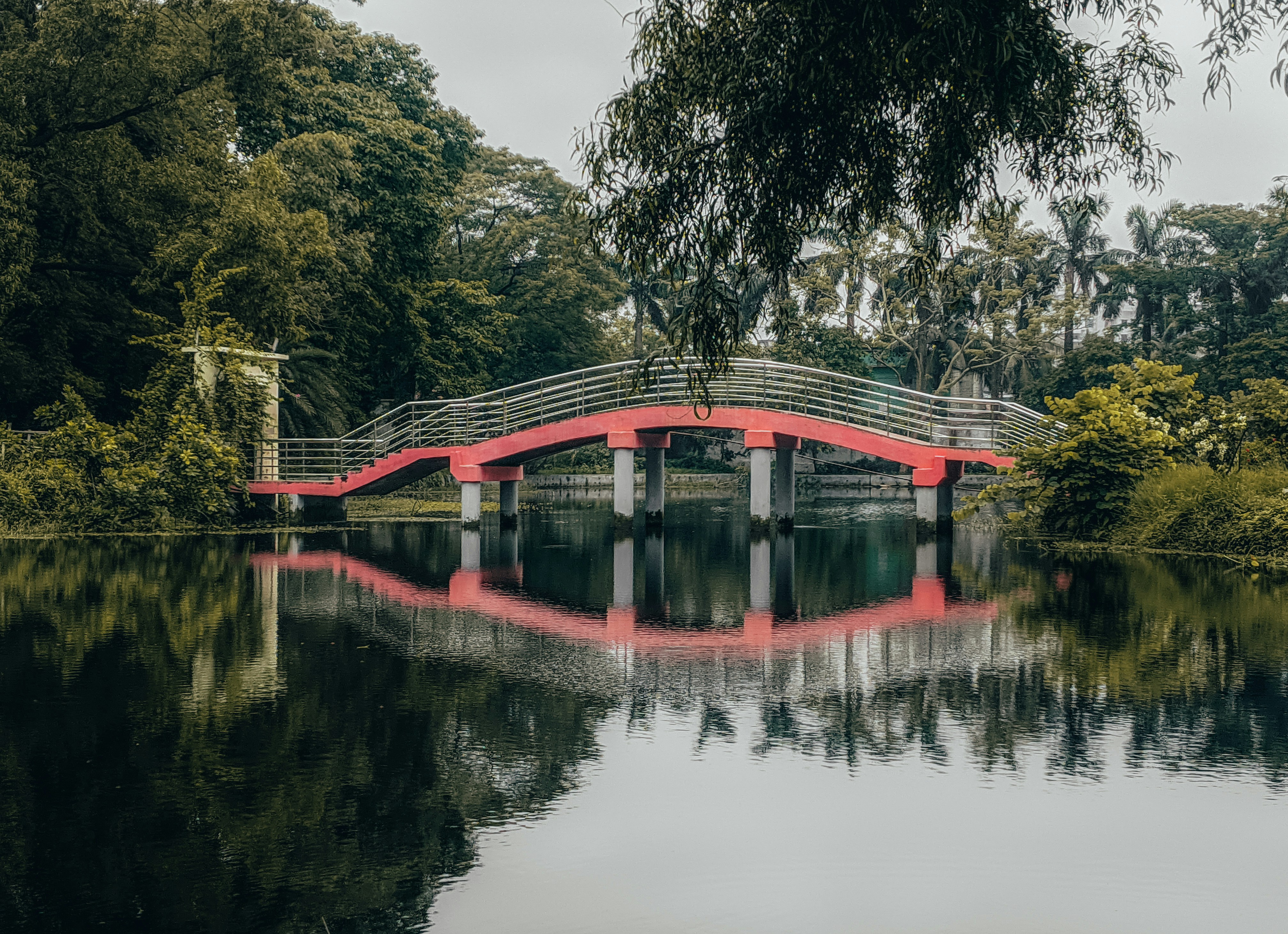 Red arched bridge mirrored perfectly in a calm forest lake surrounded by lush greenery.