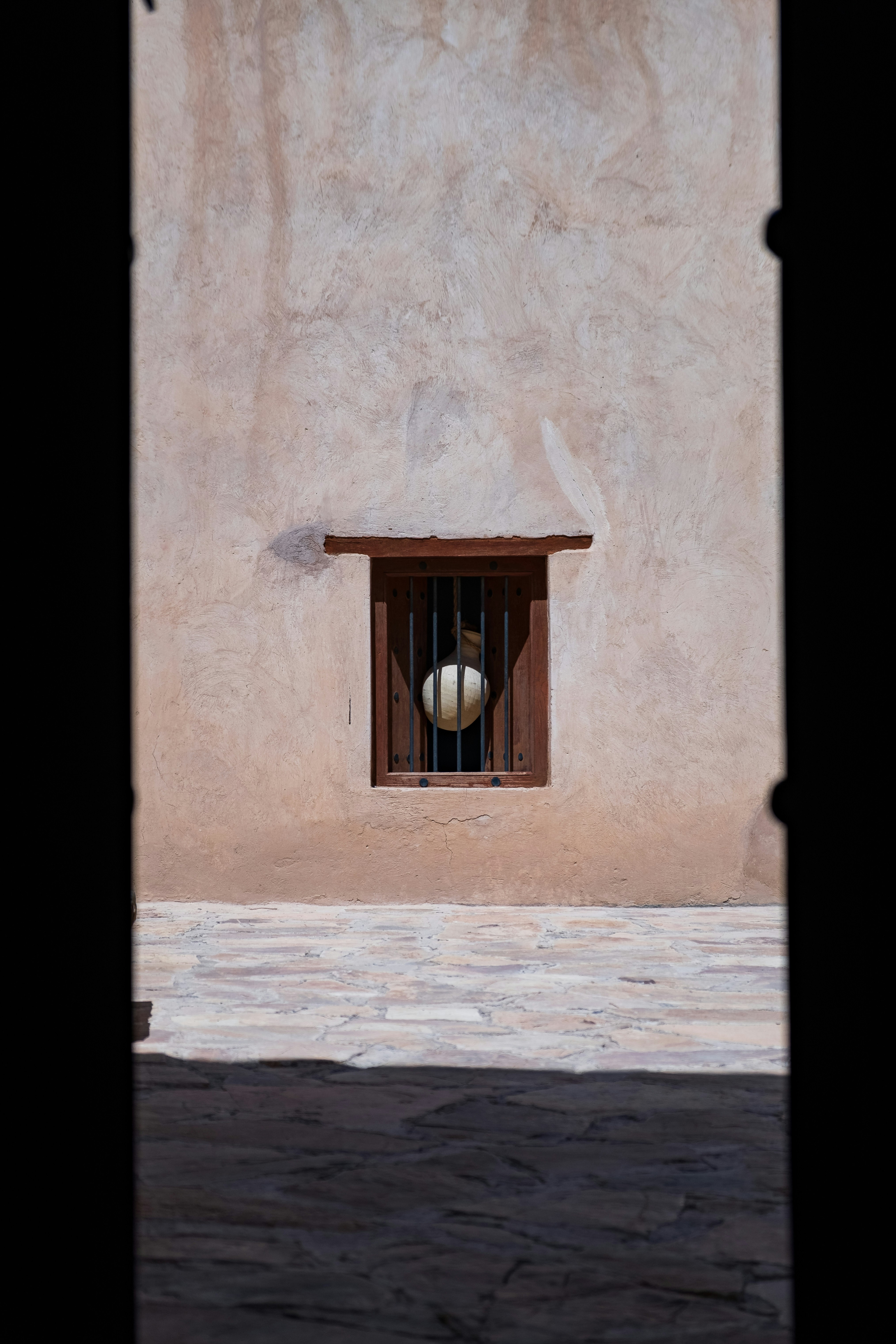 Moonlit orb behind bars: a sunlit adobe window framed by shadow