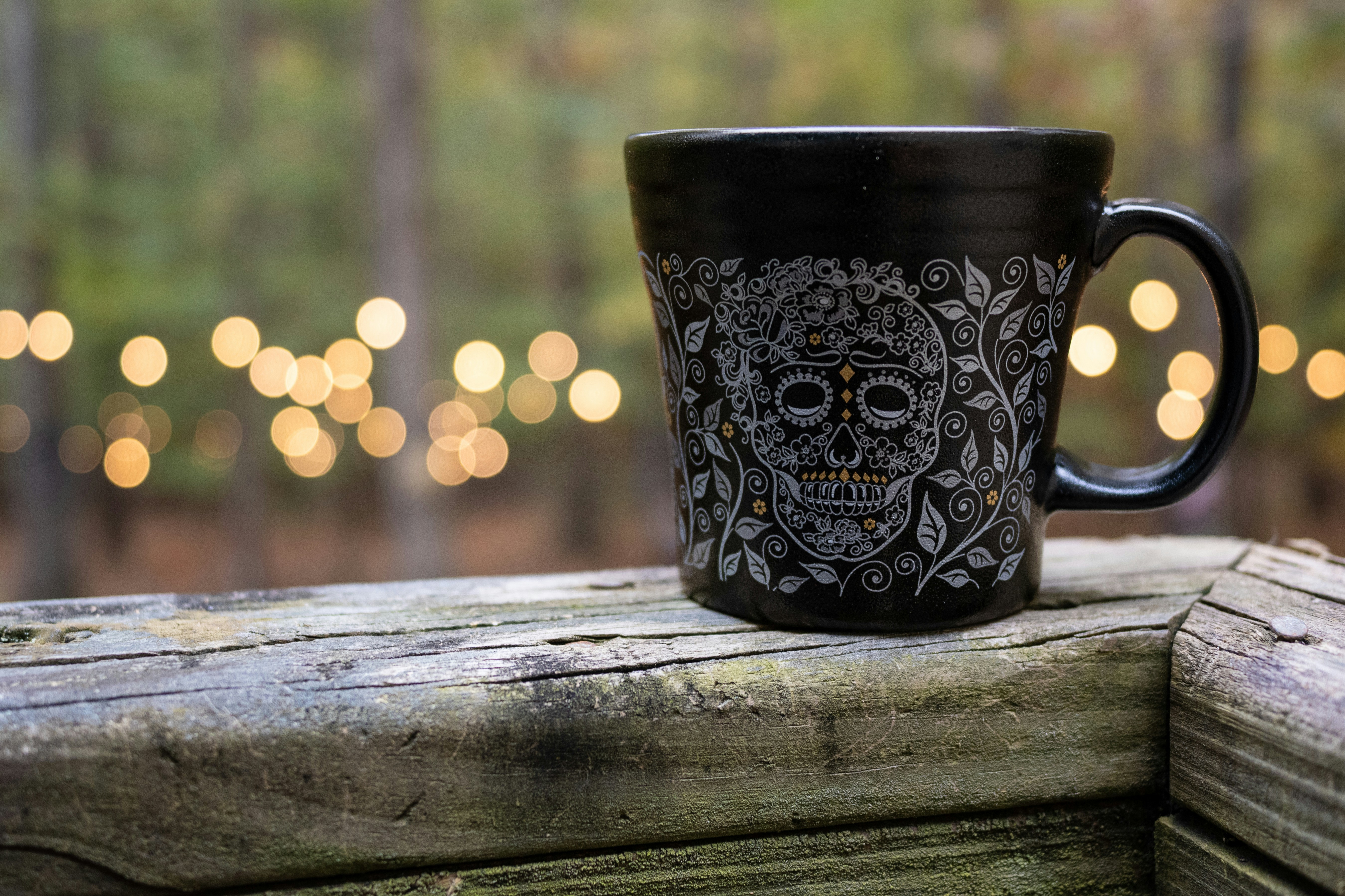 Skull-Pattern Mug Perched on Weathered Wood Amid Warm Bokeh Orbs