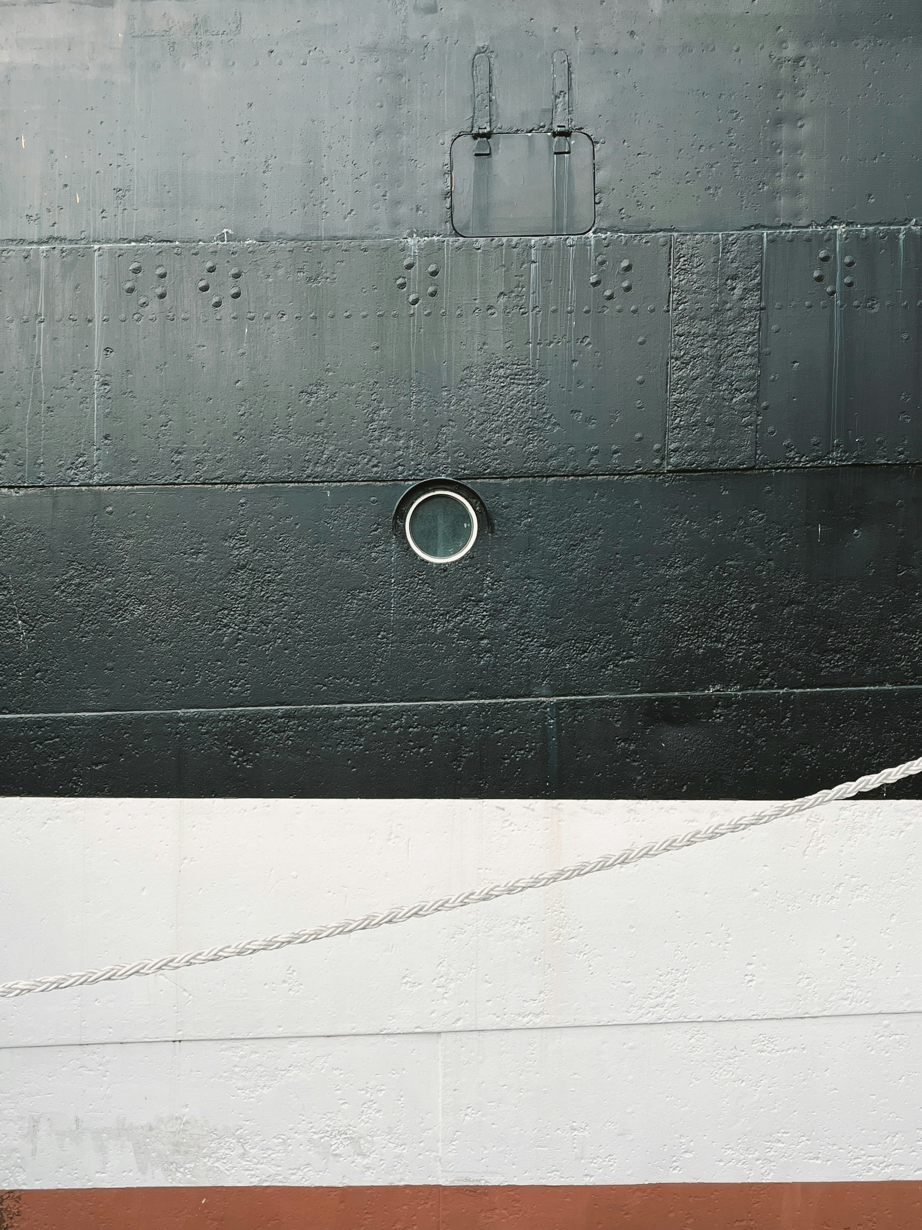 Circular Porthole on a Weathered Hull with a Diagonal Rope