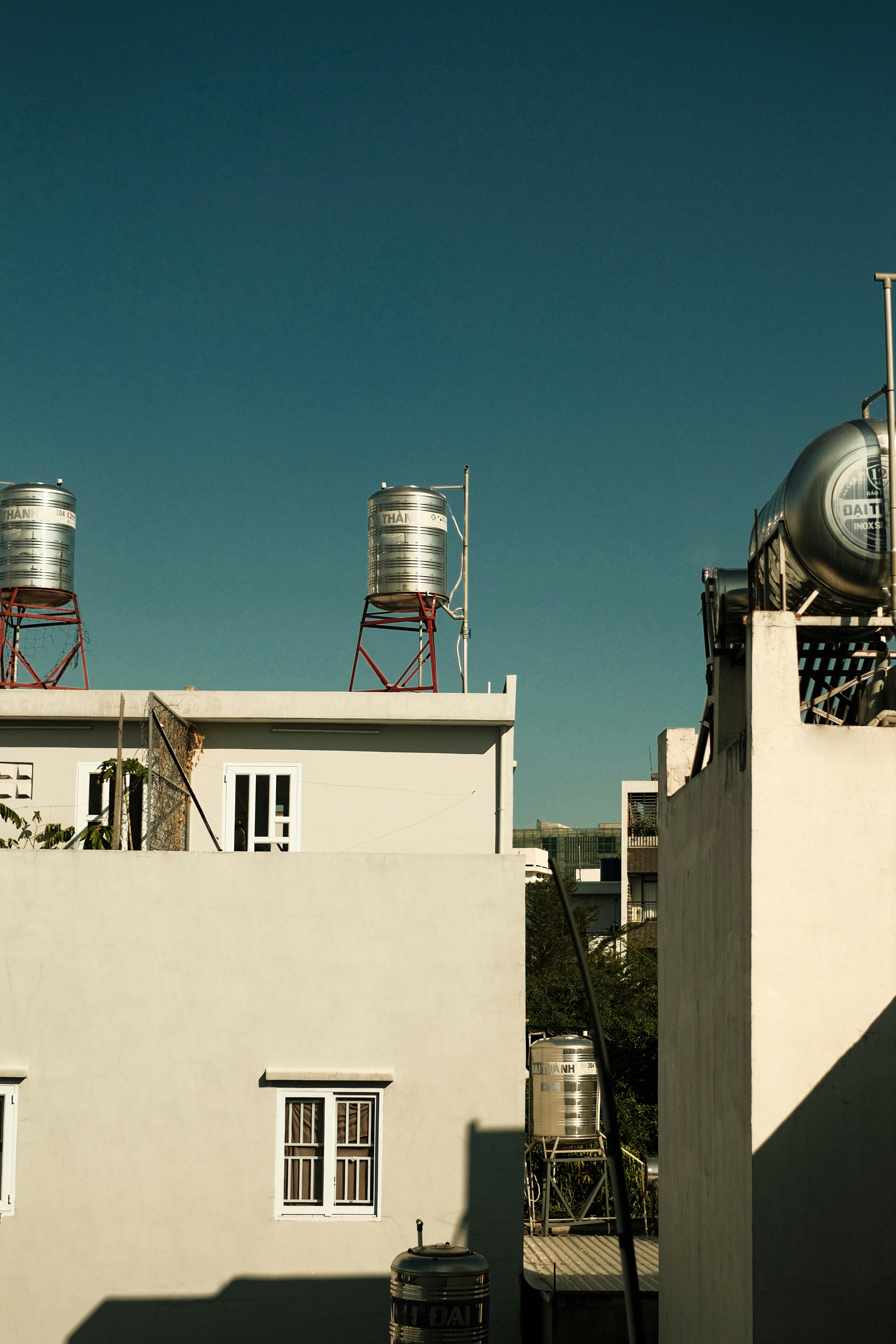 Rooftop Water Towers Rise Over a Quiet Urban Facade Under a Teal Sky