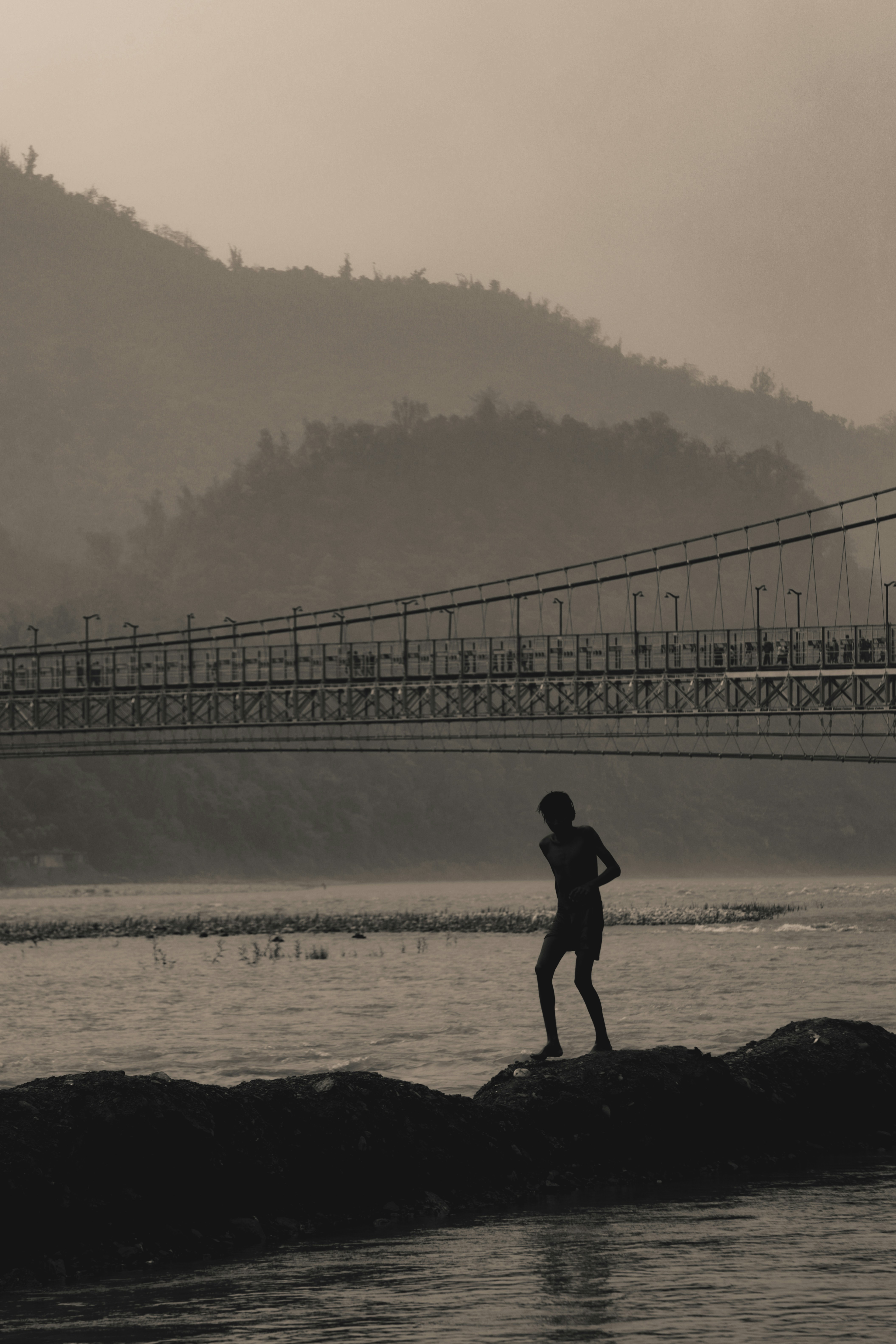 Silhouette on the Rocks Beneath the Suspended Bridge at Dusk