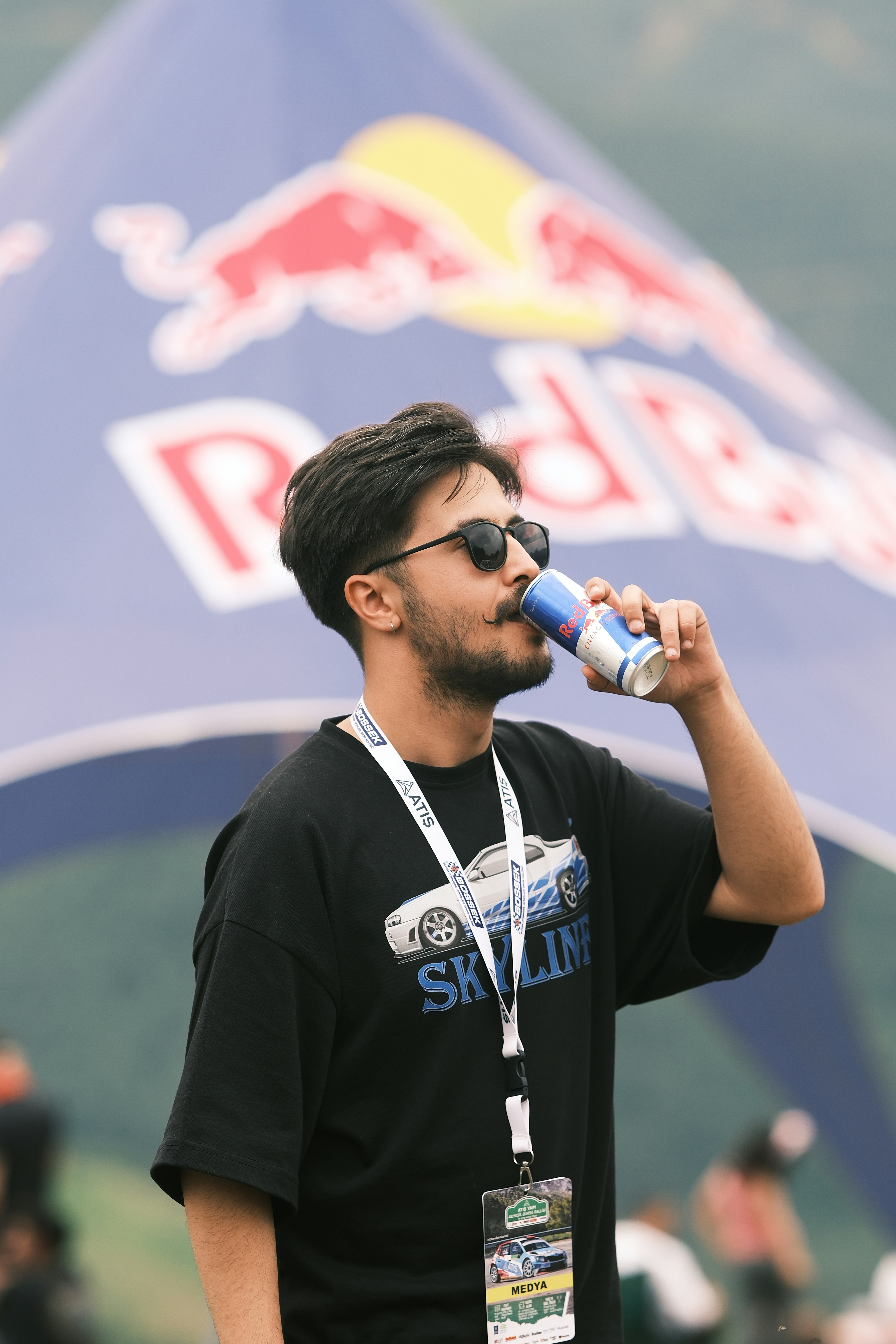A man drinking from a bottle while standing in front of a red bull tent ...