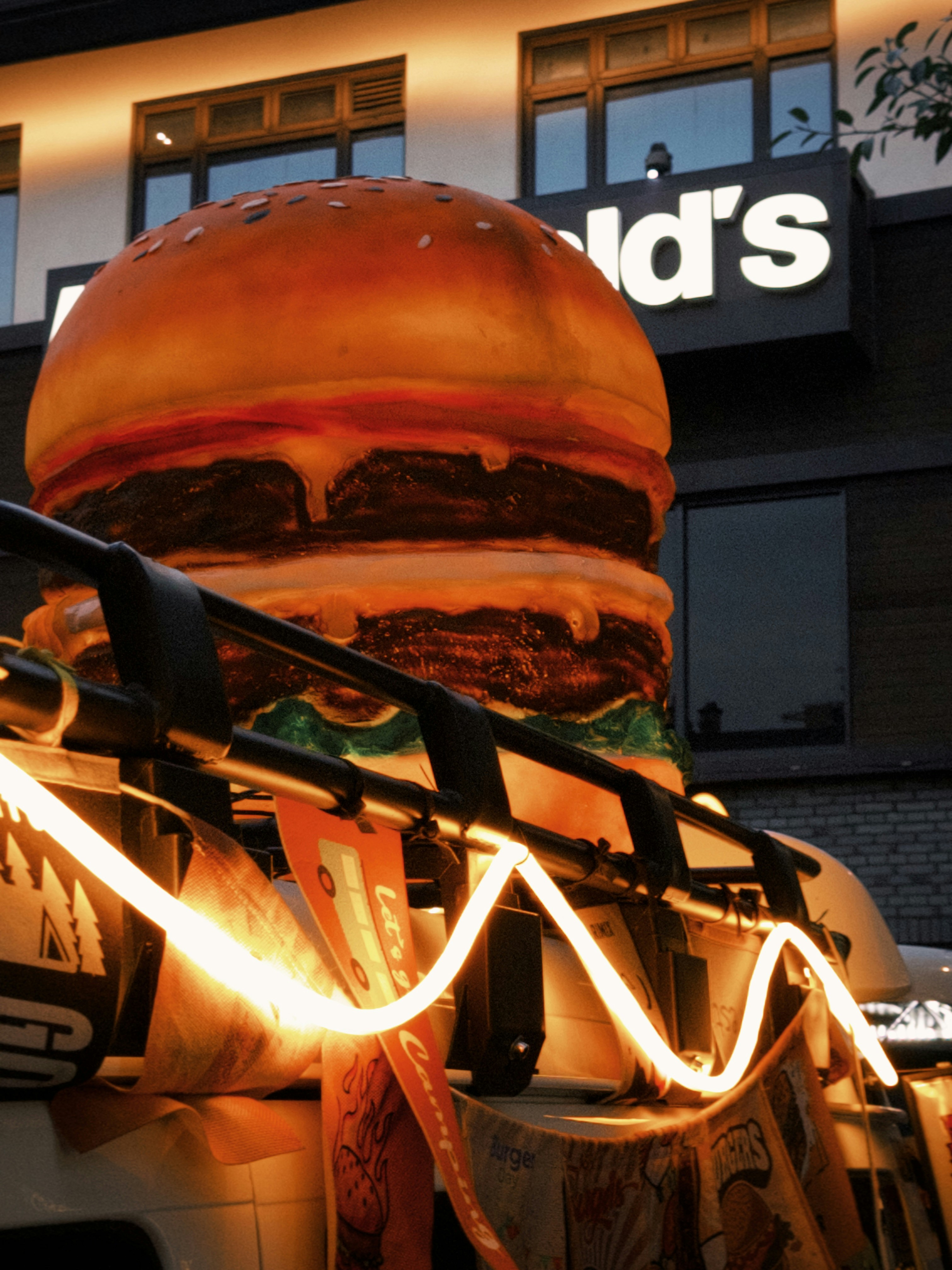 Giant Hamburger Prop Illuminated by Neon Cords Above a Food Truck at Dusk