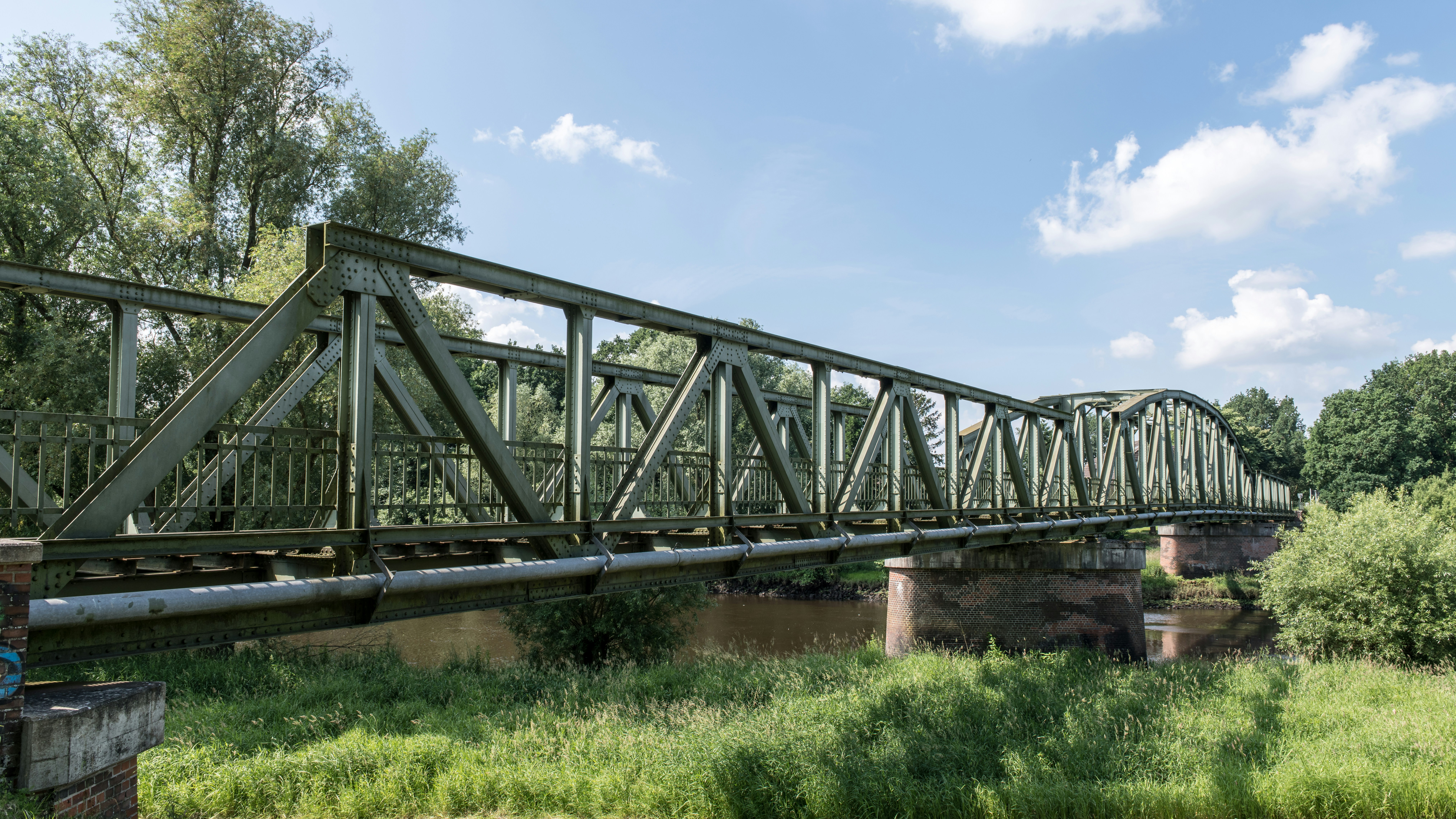A large metal bridge over a river next to a forest photo – Free Winsen ...