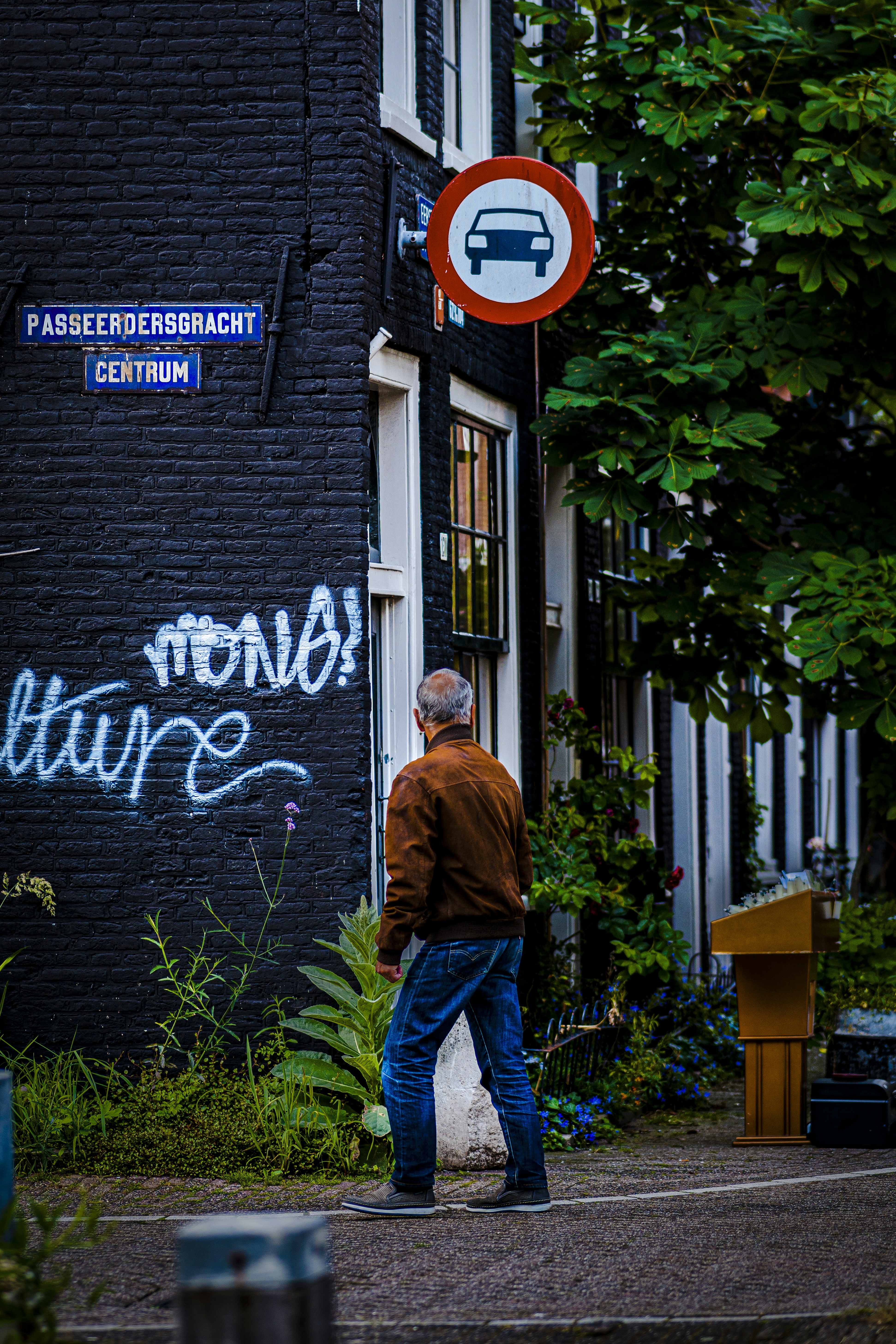 Urban Quiet: A Man in a Brown Jacket Walking Past a Graffitied Wall