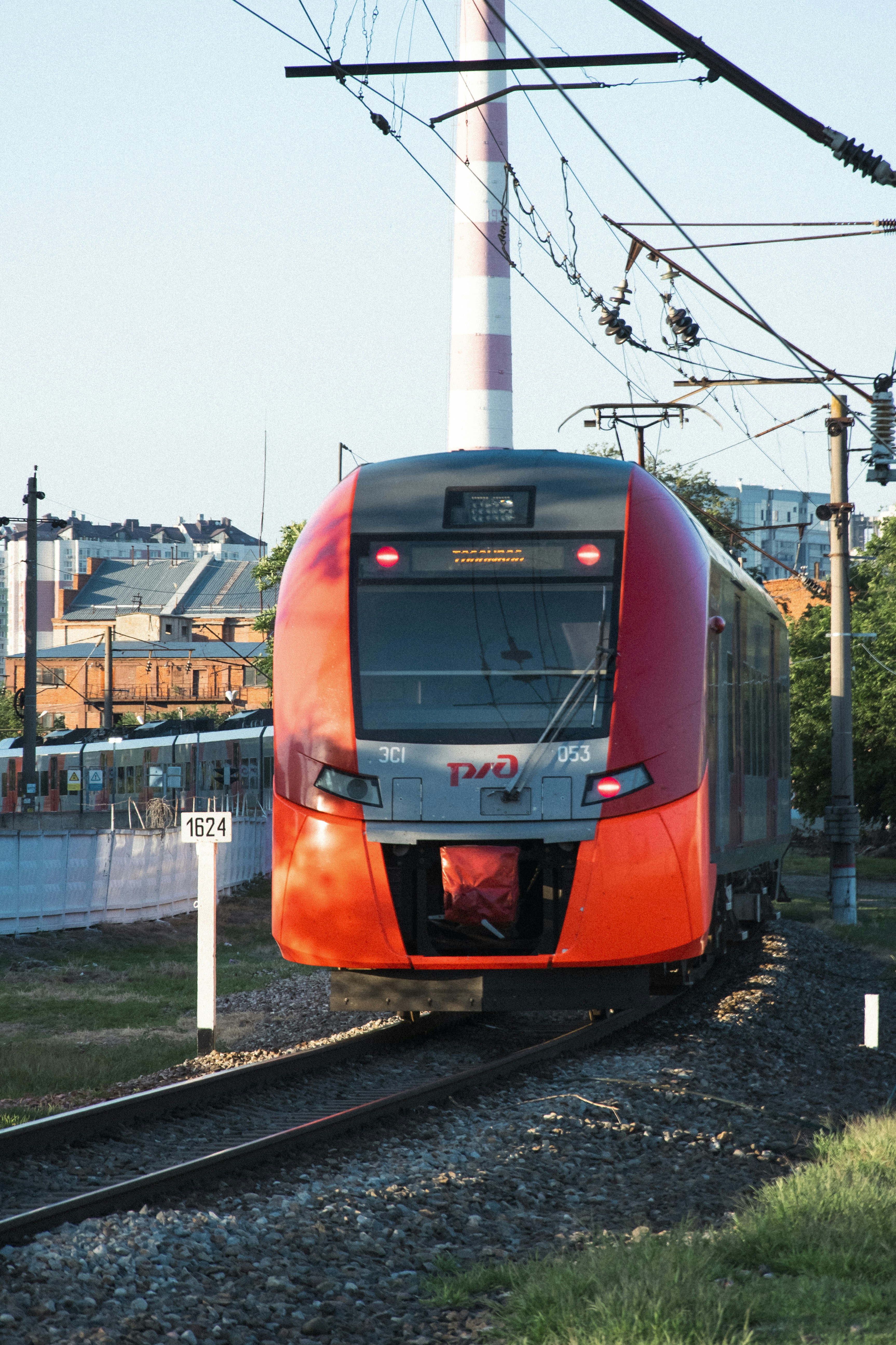 Un tren rojo viajando por las vías del tren junto a un exuberante campo ...