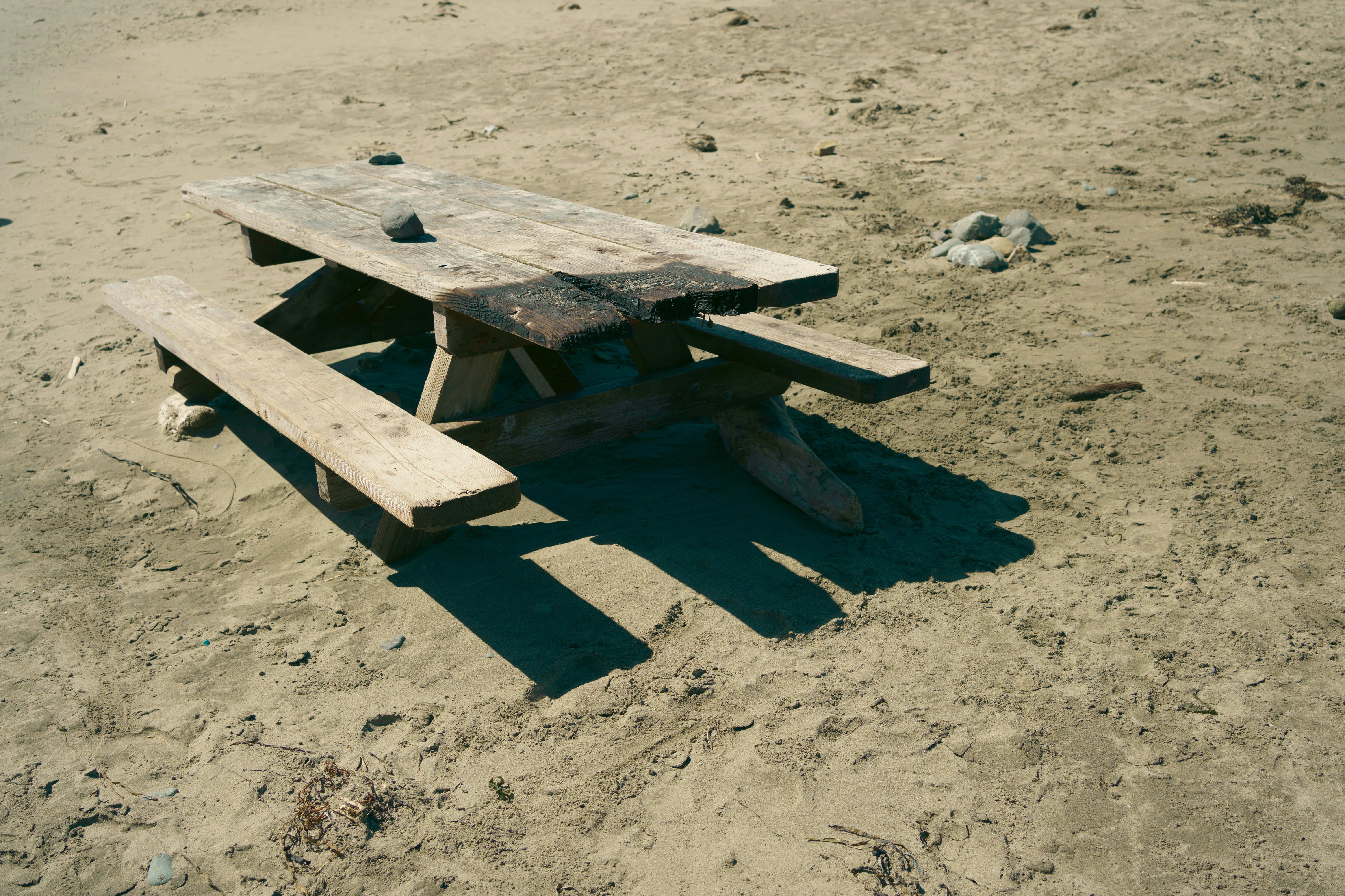 Weathered Picnic Table Casts Long Shadows on a Sun-Baked Beach