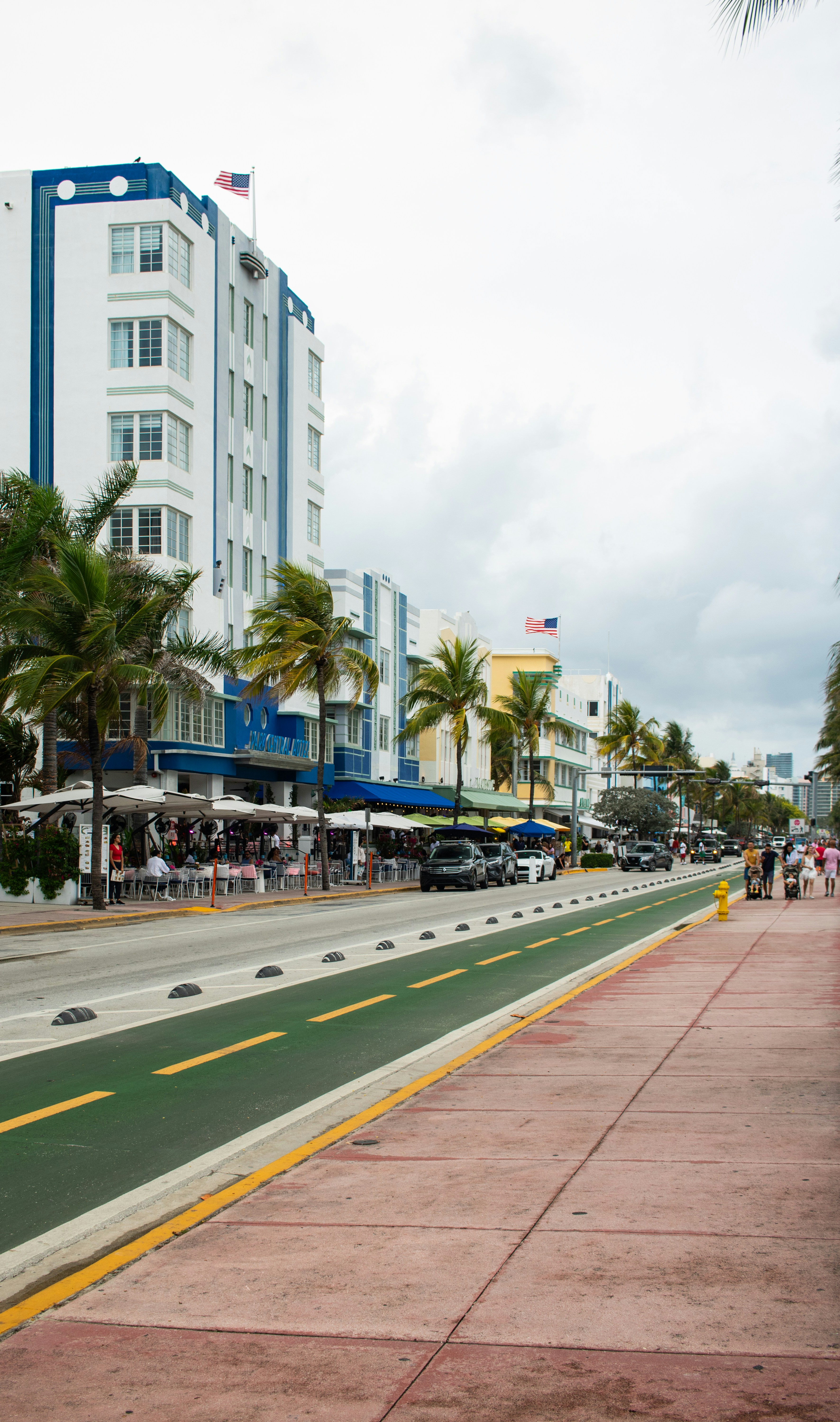 Vibrant streets lined with palm trees and art deco architecture in a bustling coastal city. The scene captures the lively atmosphere of urban life by the beach.
