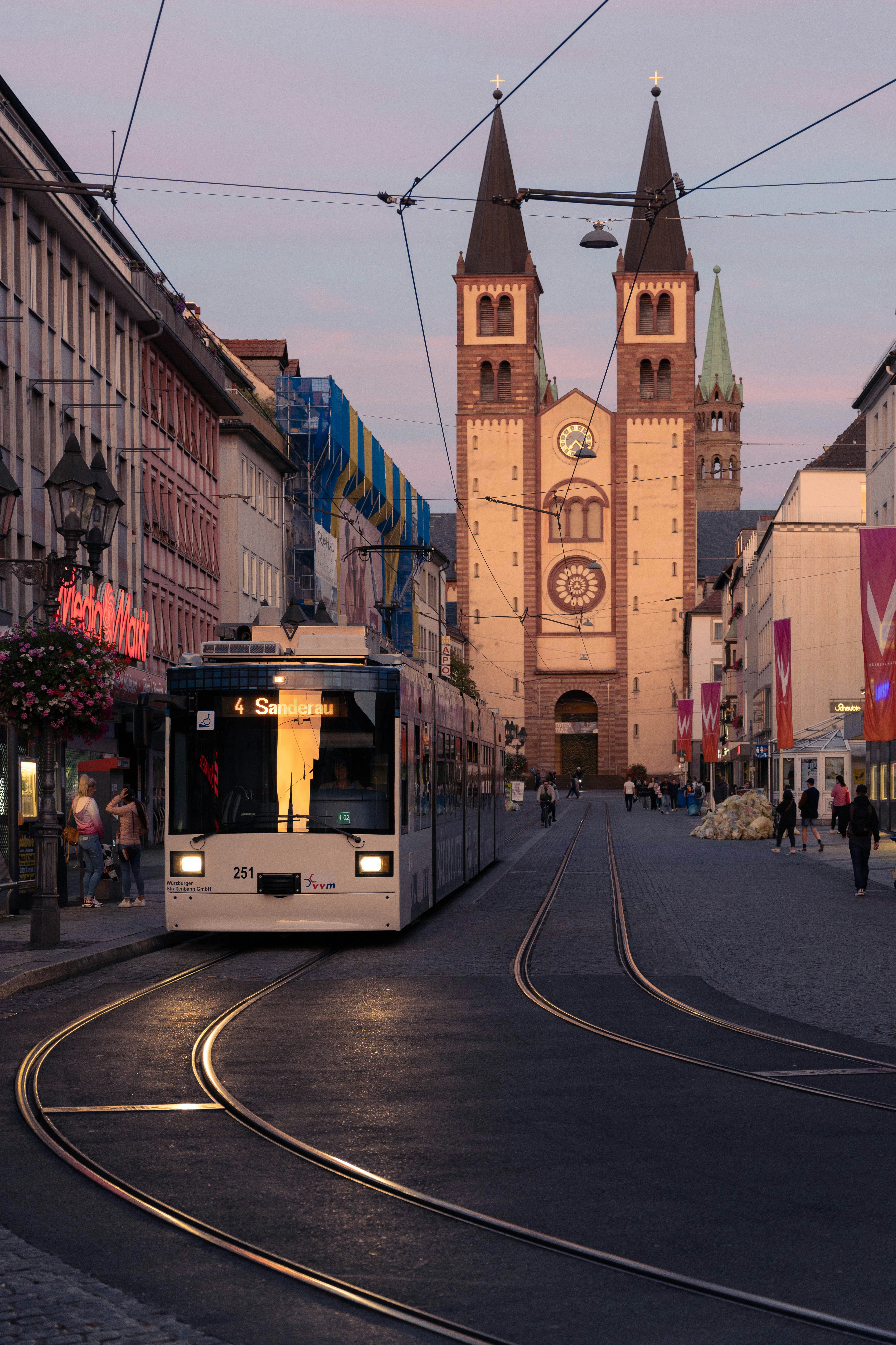 Tram gliding through a city street towards a majestic cathedral at dusk.